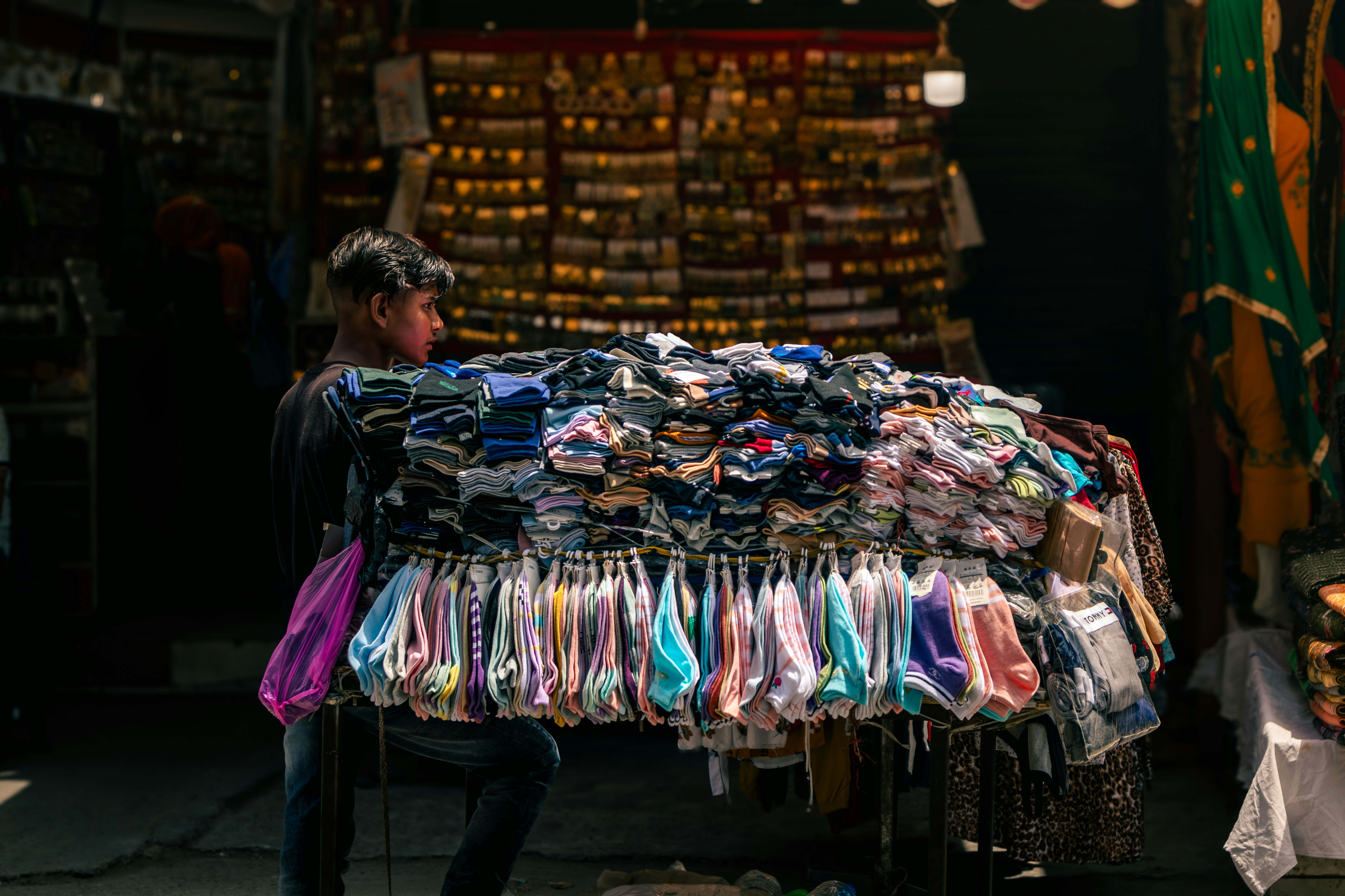 Market Stall Symphony: A Seated Vendor Surrounded by Tidy Piles of Colorful Scarves