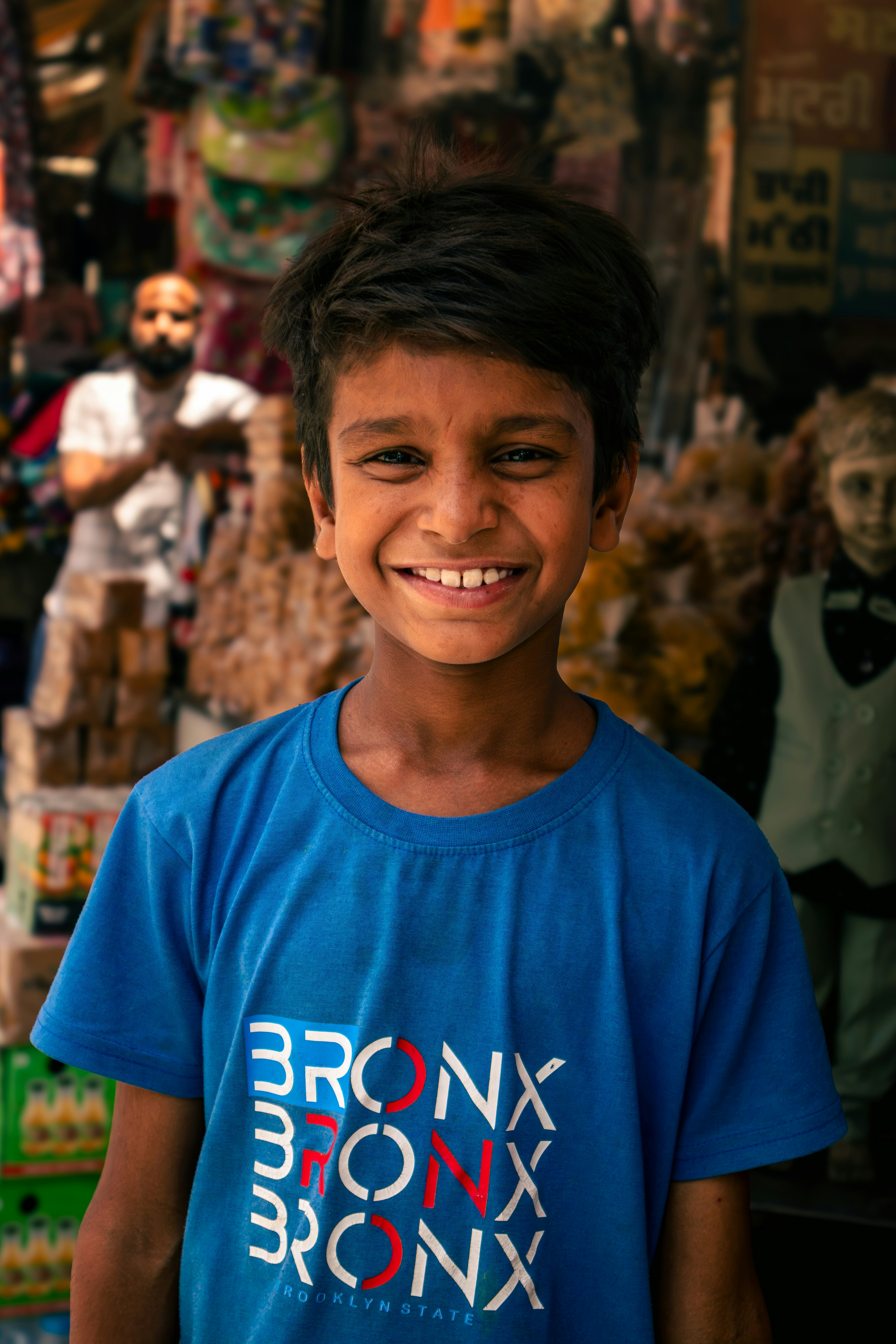 Smiling Street Kid in a Busy Market, Blue Tee Reading Bronx on the Front