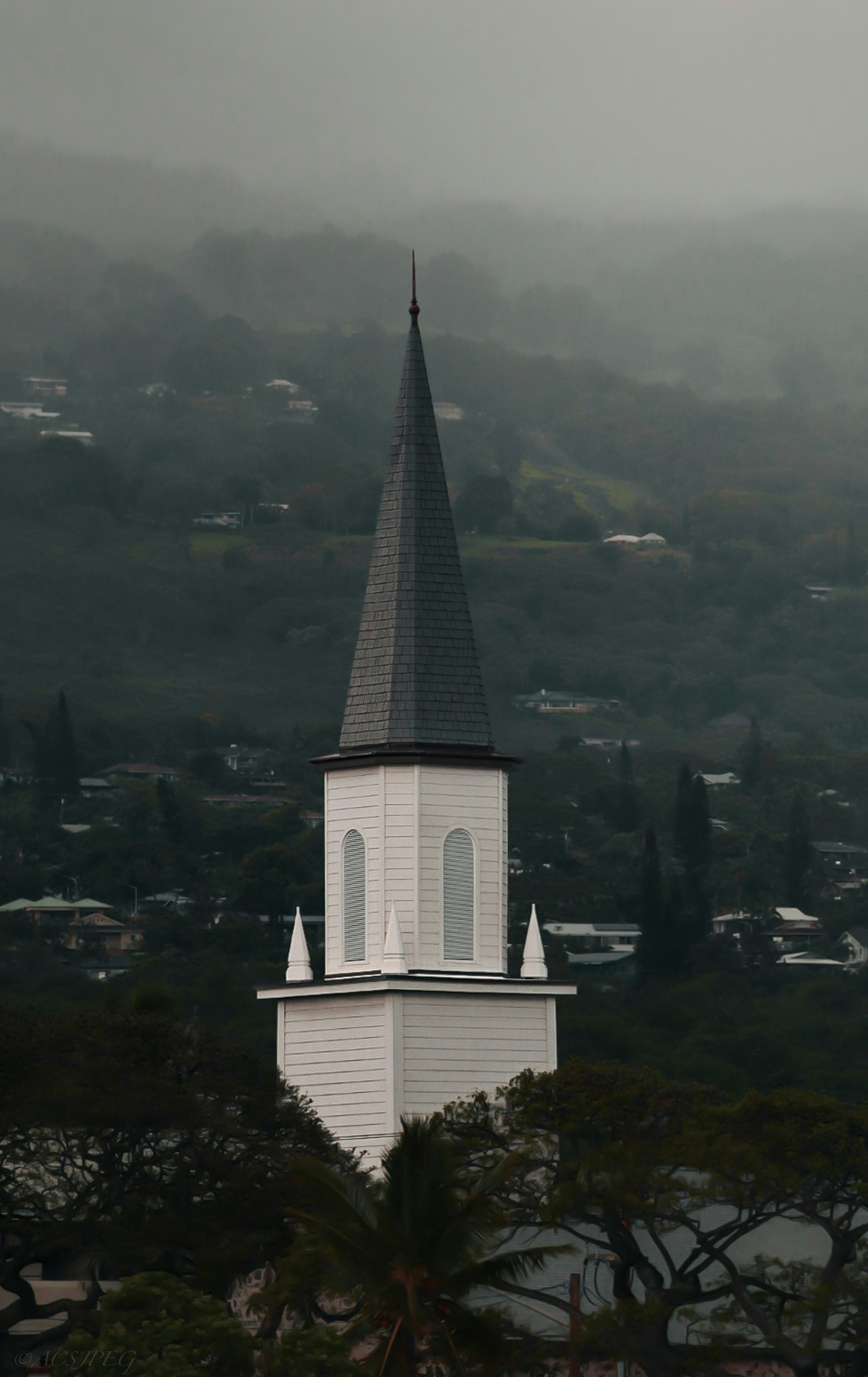 White church steeple against misty green hills.