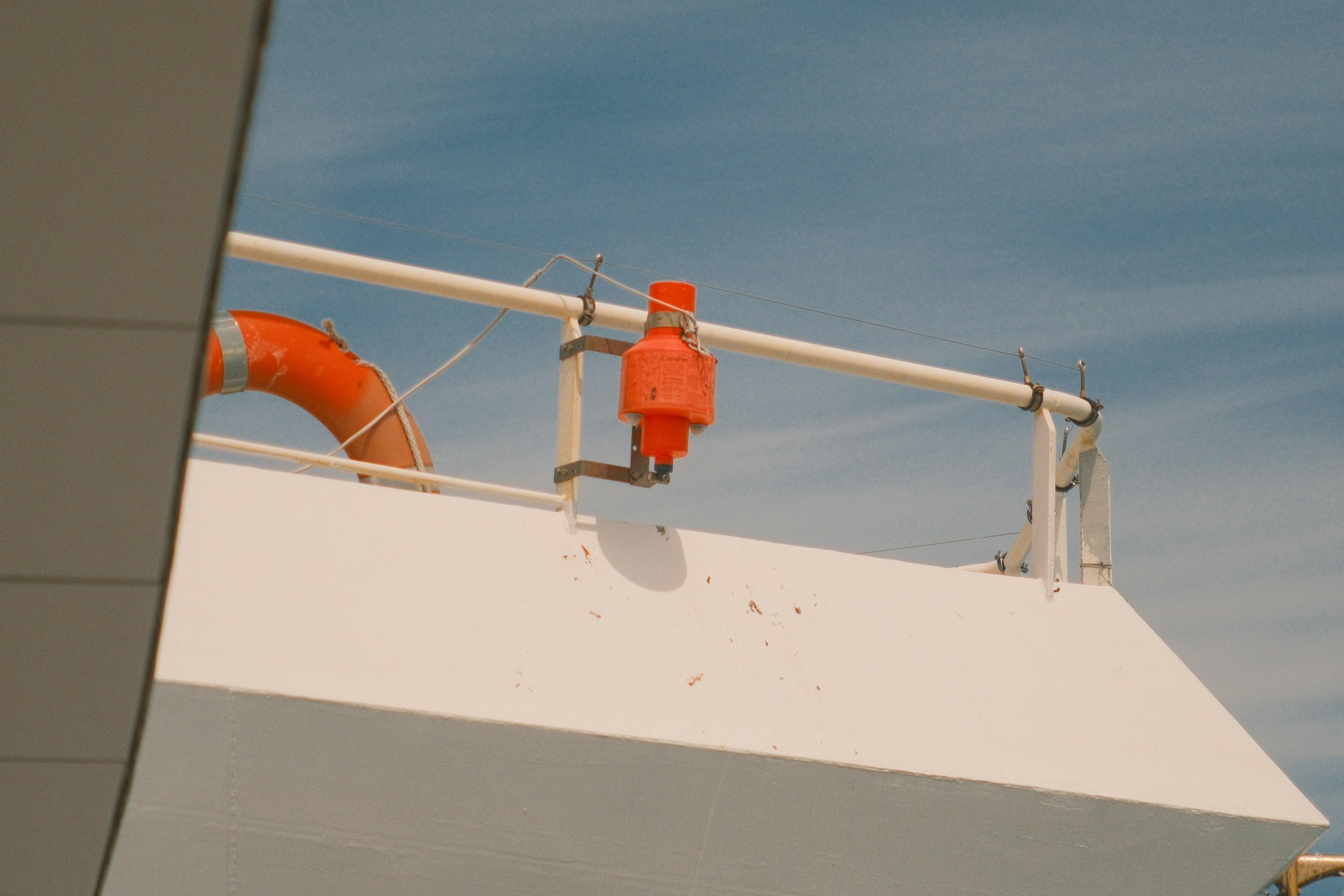 Orange lifebuoy and beacon perched above a pale ship deck against a clear blue sky