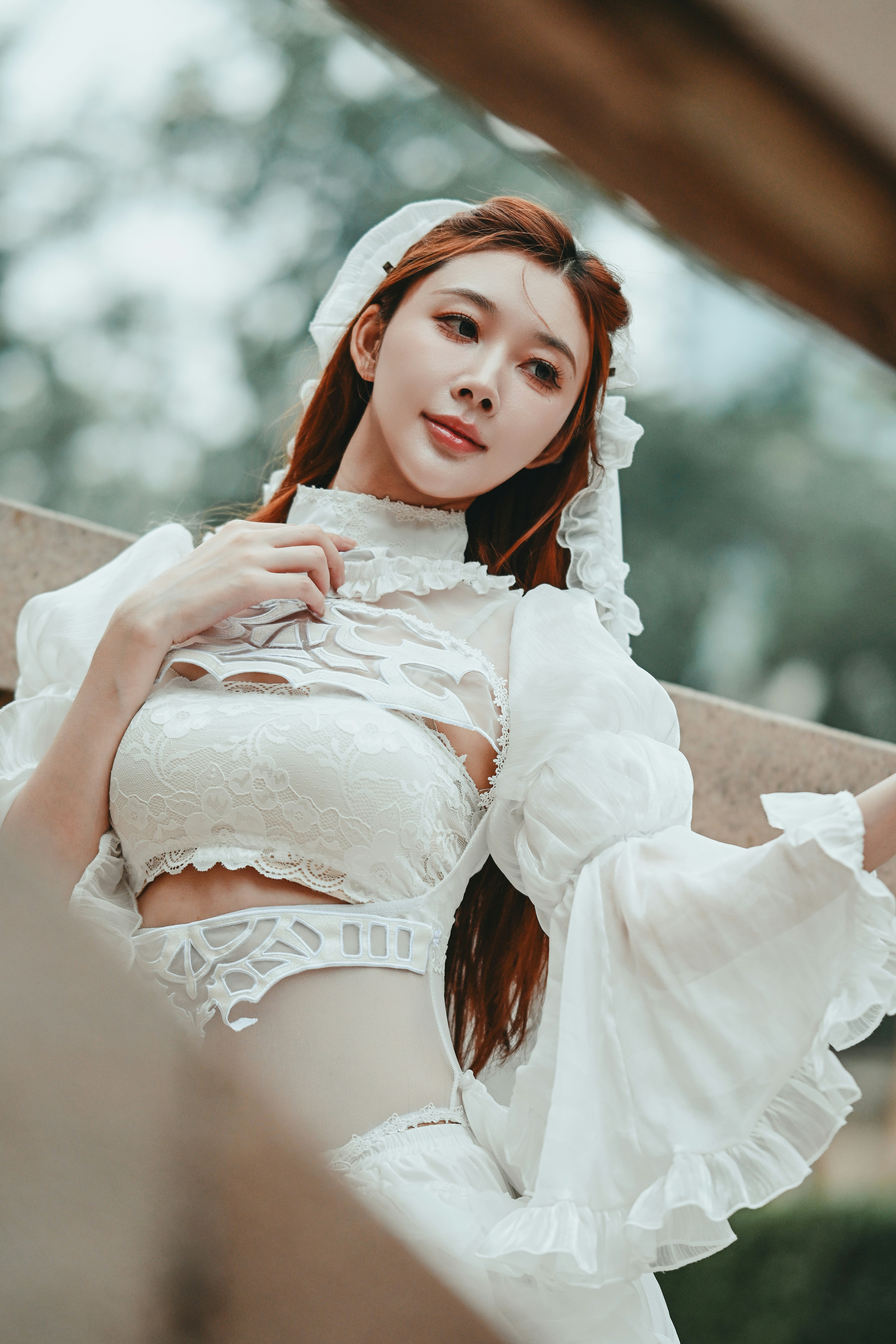 A young woman in a white lace outfit poses outdoors.