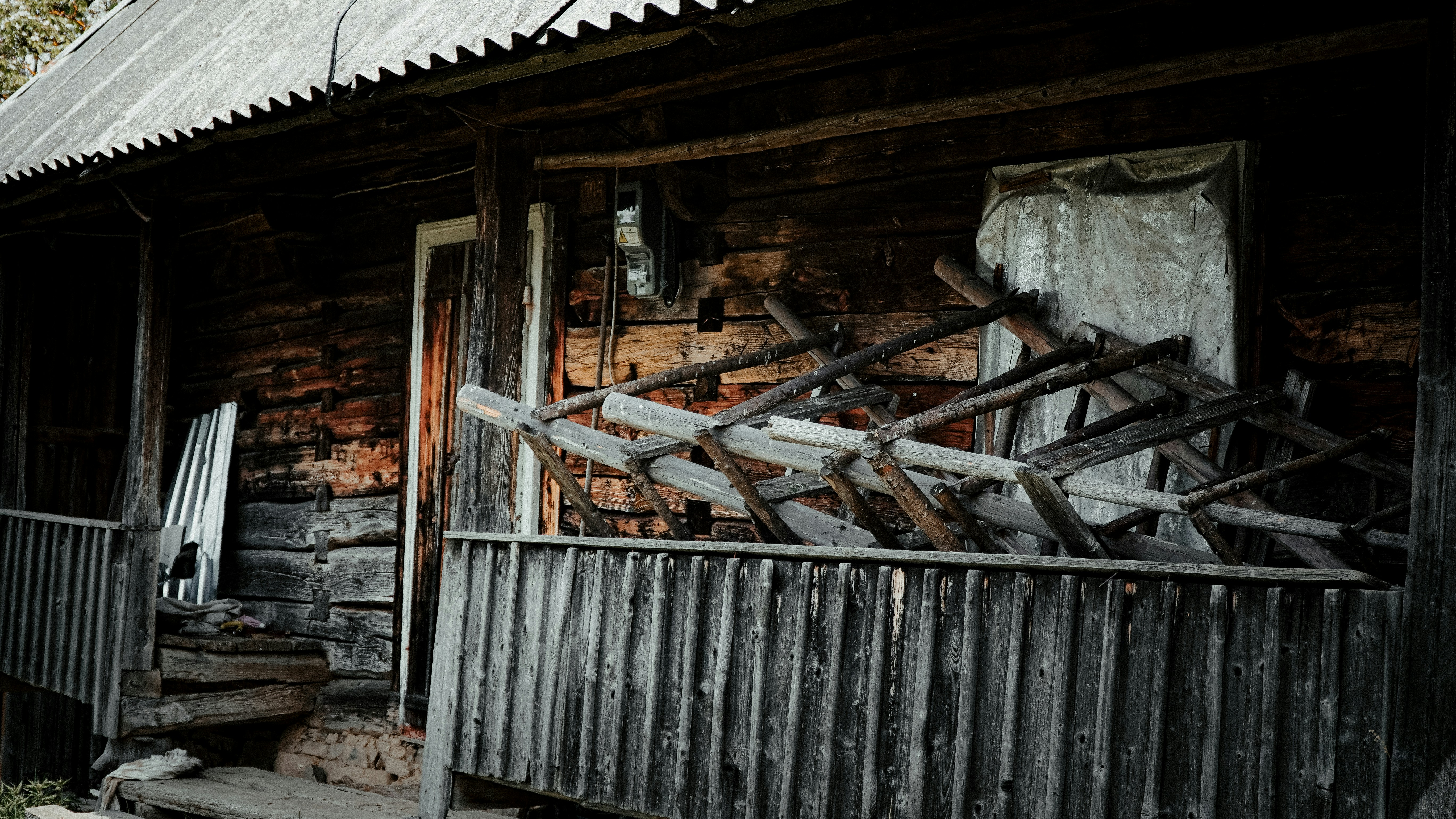 Weathered Cabin, Stacked Timber, and Faint Light in a Ruinous Porch