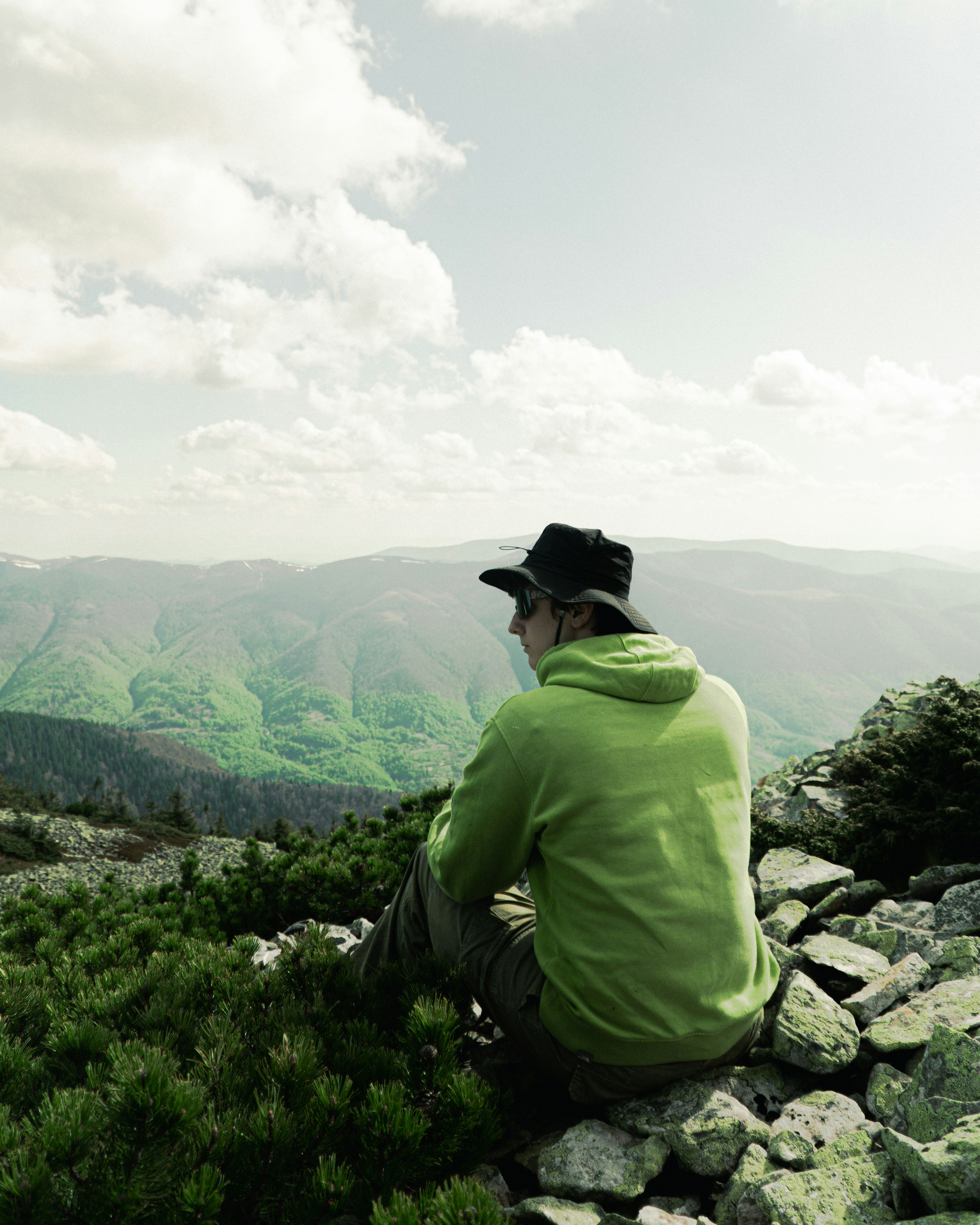 Green-hooded hiker at a sunlit alpine edge