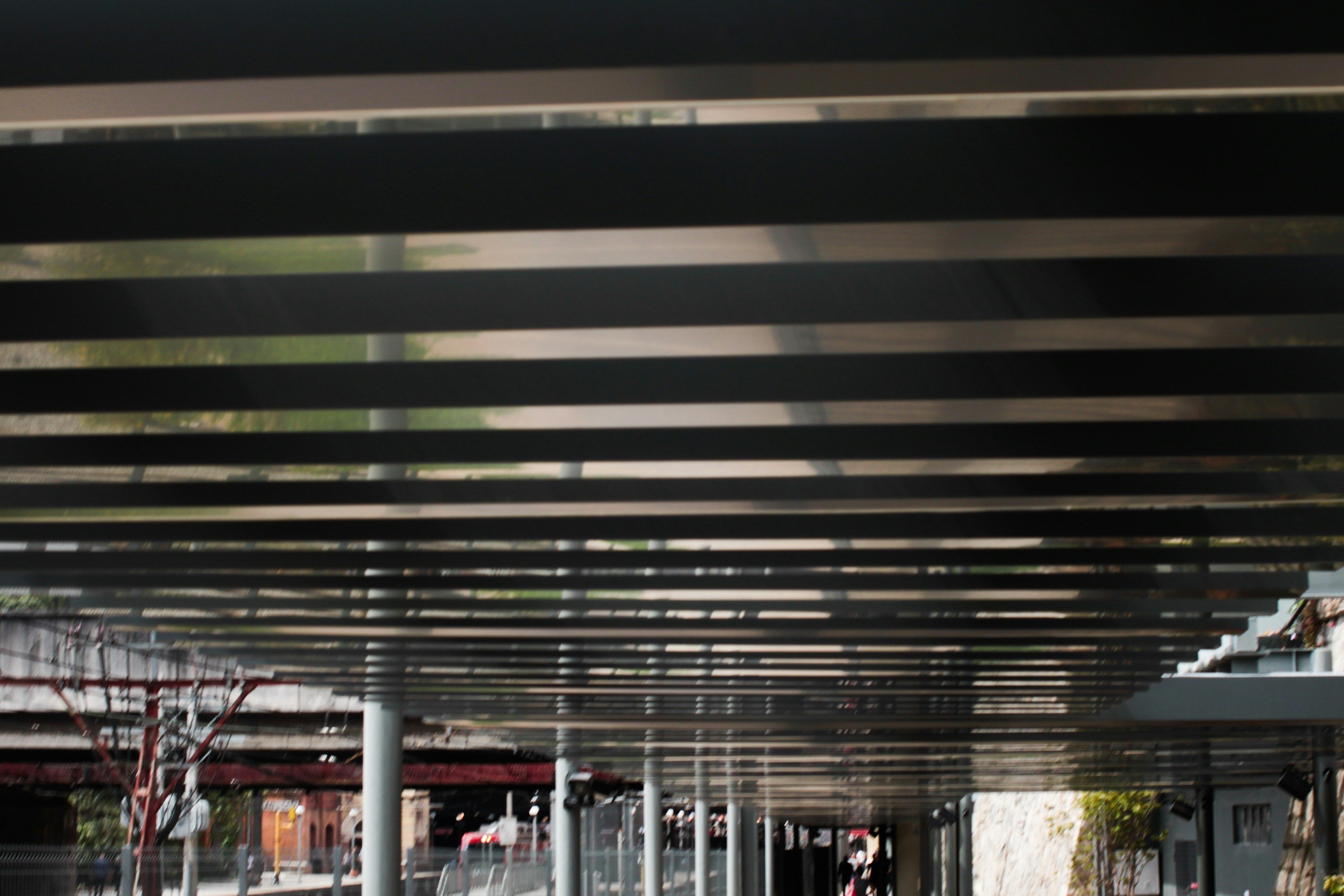 Urban walkway beneath horizontal slats, showing support columns and pedestrians at the far end.