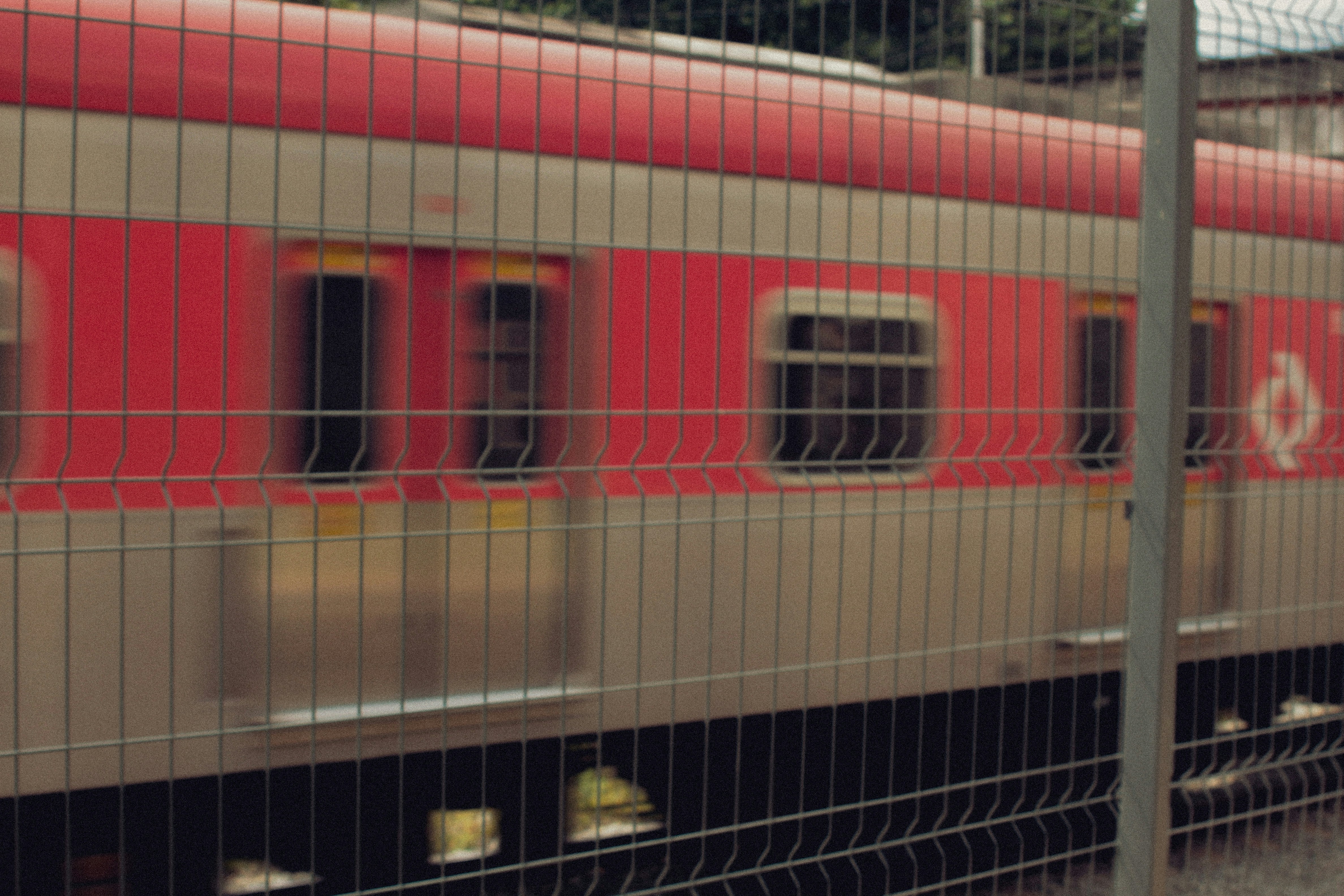 Fenced View: Blurred Red Car in Transit