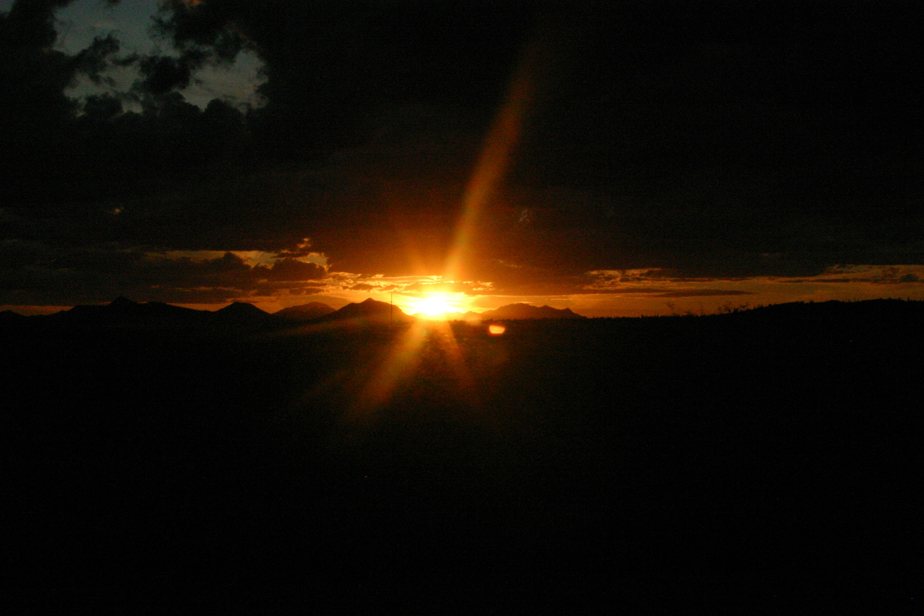Golden sun setting over dark mountain silhouettes with bright rays.