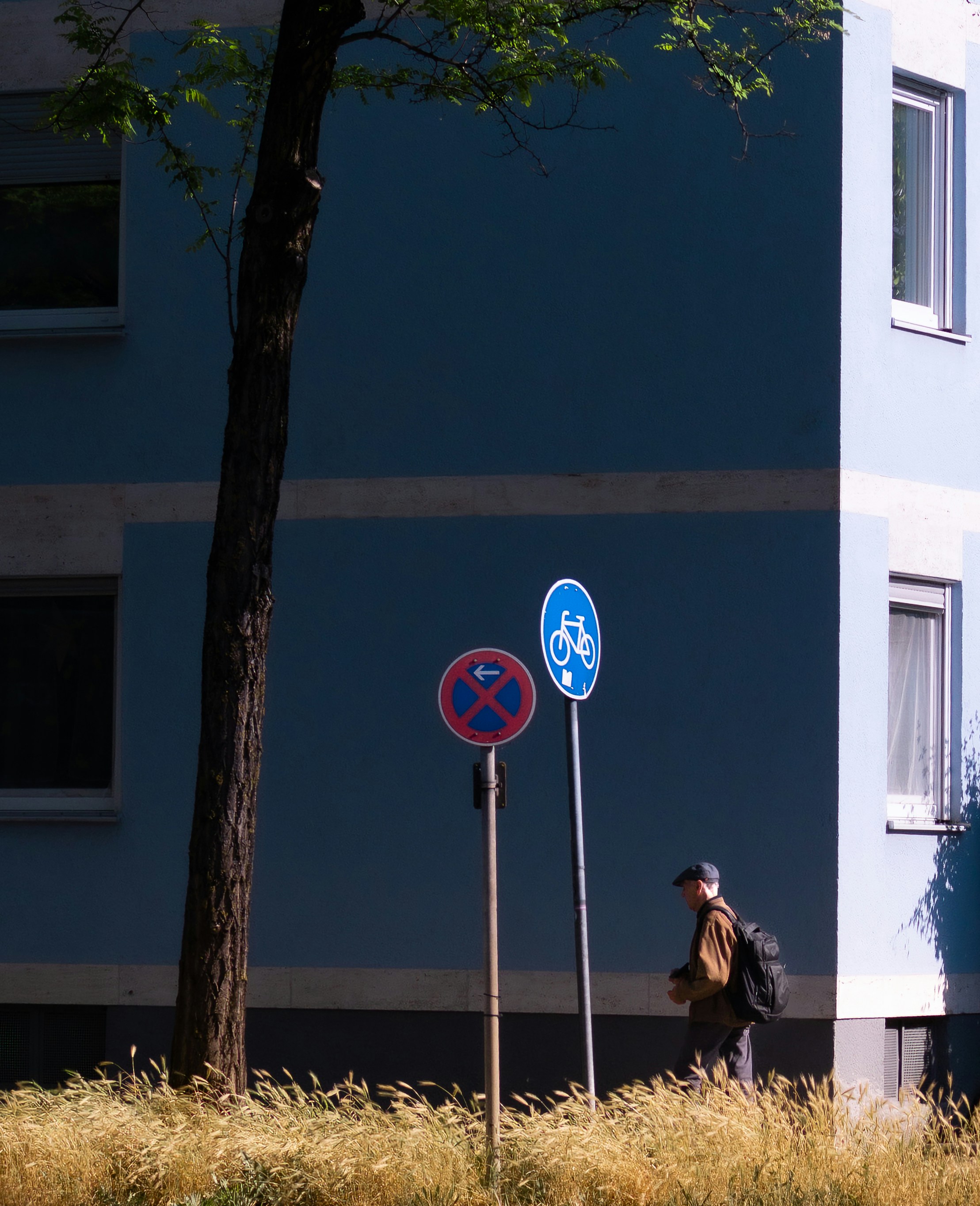 Pedestrian with backpack passes a blue-sign contrast against a blue building