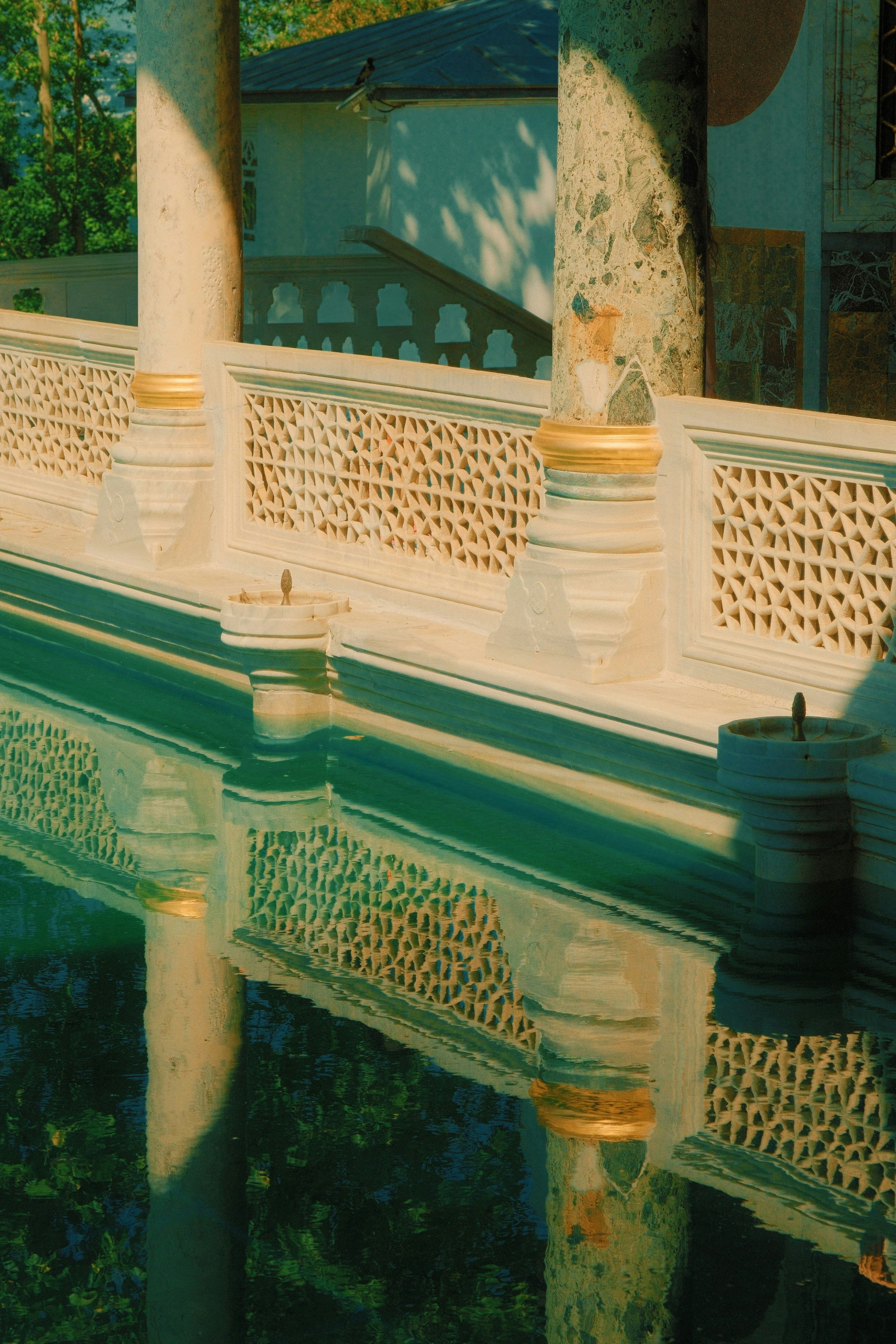 Ornate white balustrade reflecting in calm, green-tinted water.