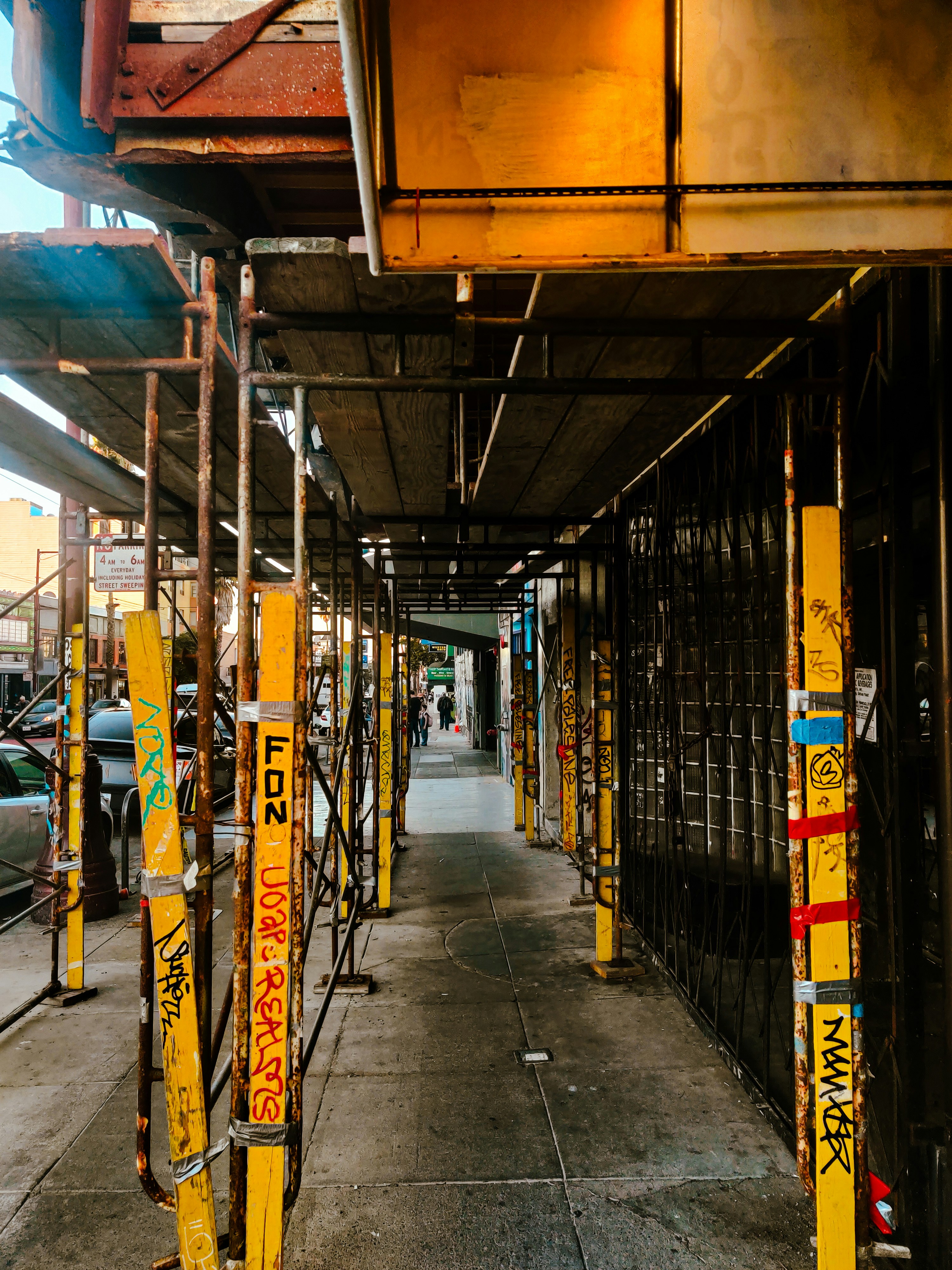 Under the Urban Scaffold: A Narrow Corridor of Colorful Poles and Graffiti