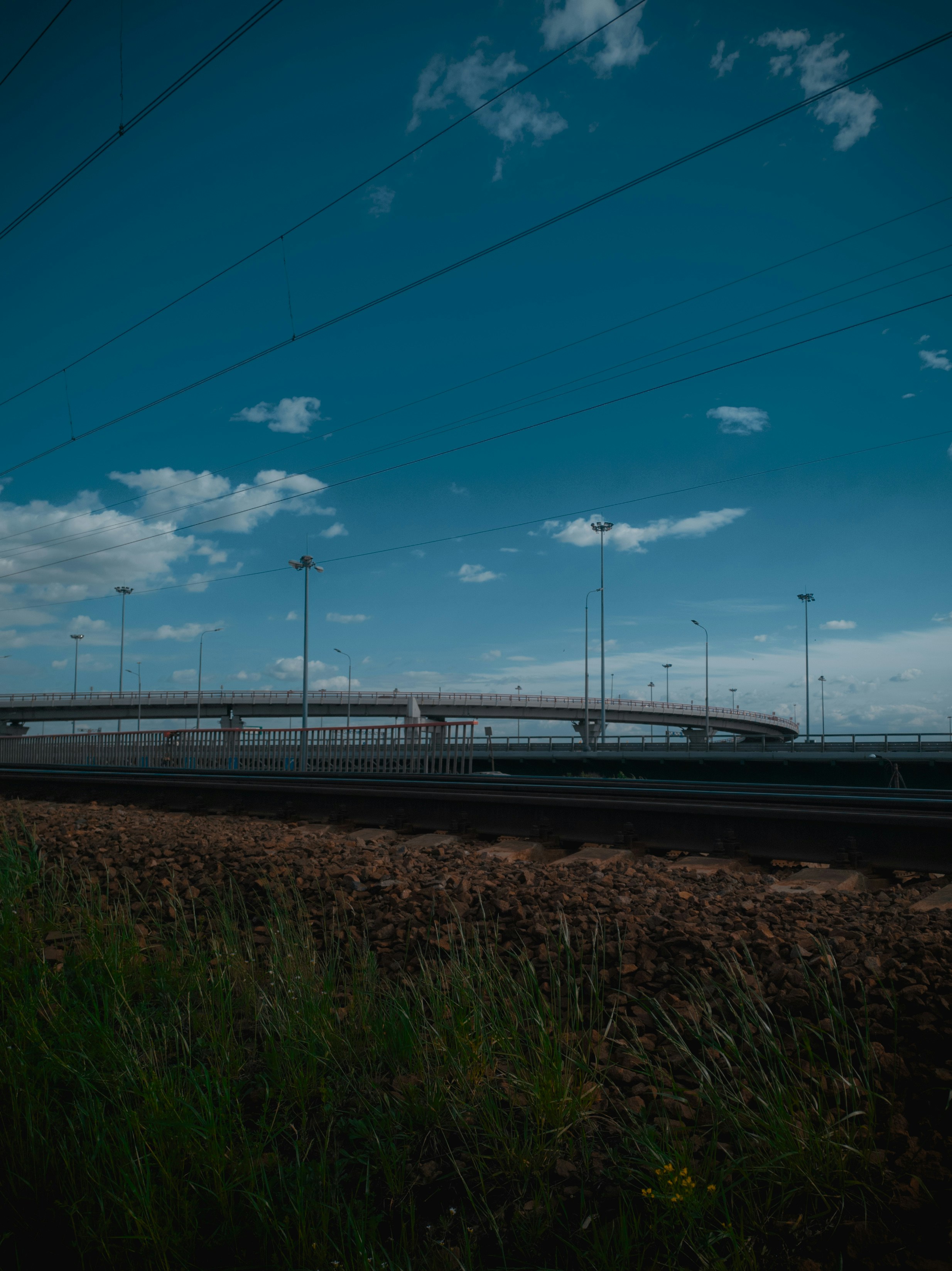 Overpass Amid Vast Sky: Rails, Lights, and Quiet Grass