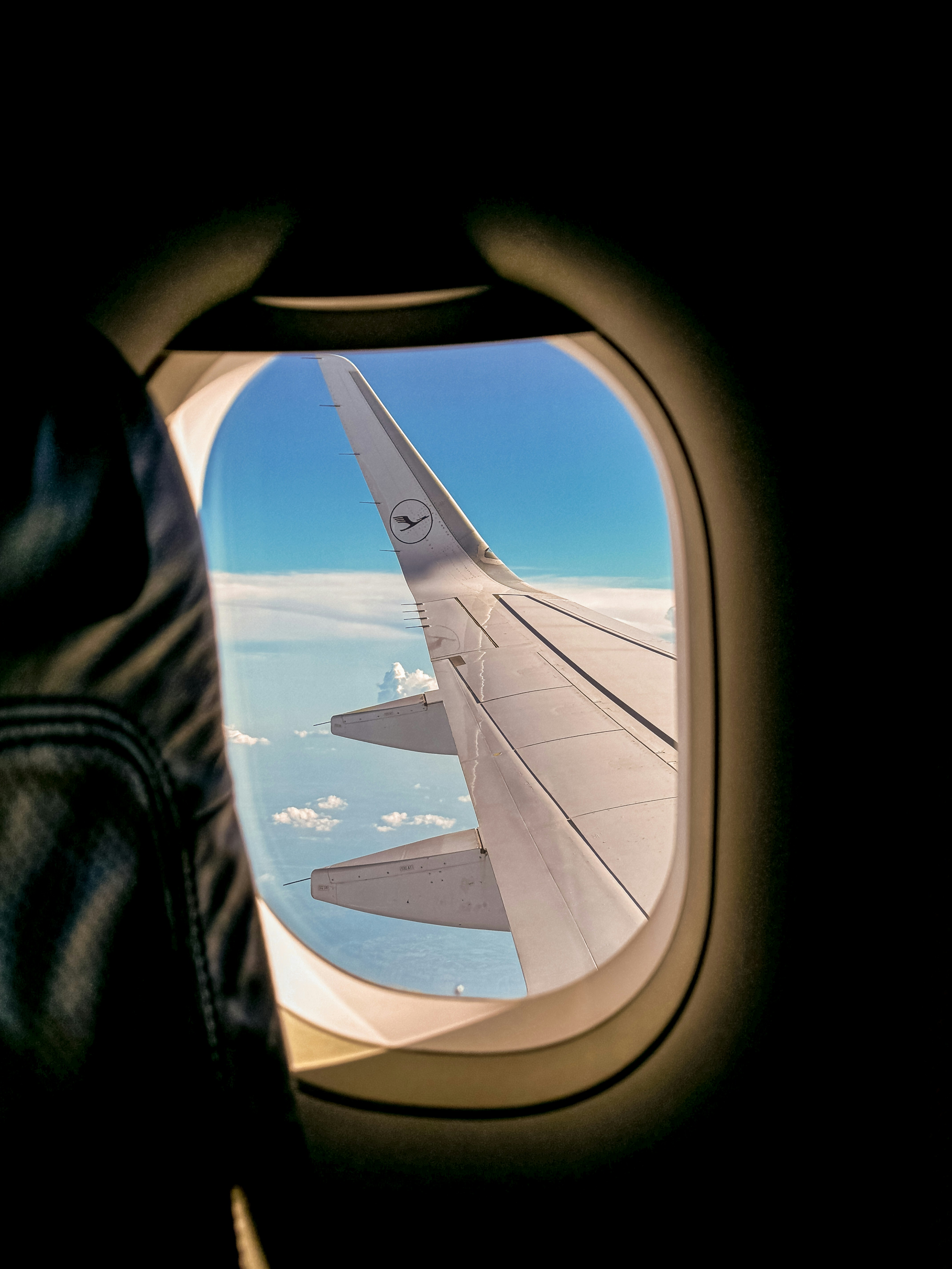 View of airplane wing, clouds, and blue sky from window.