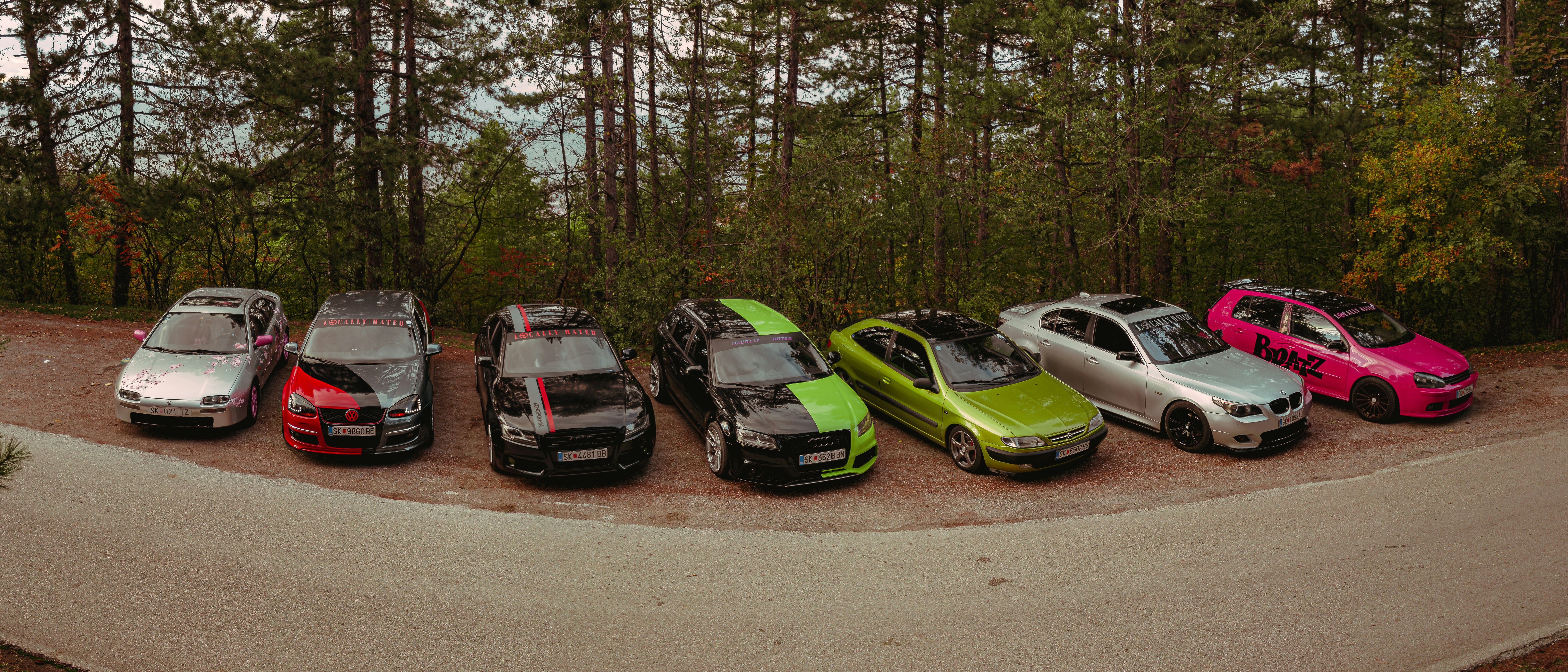 Seven colorful cars parked in a row outdoors near trees.