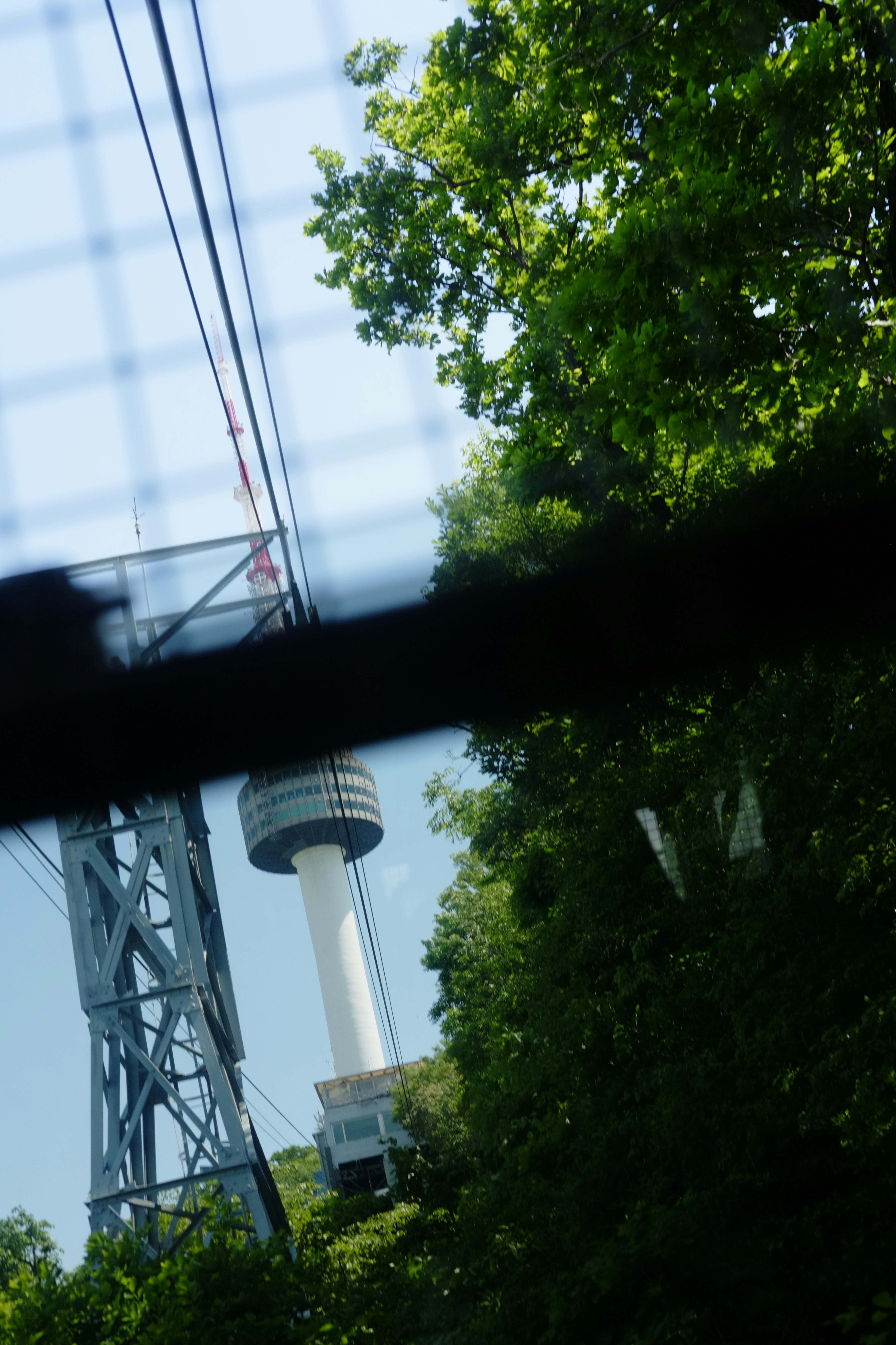 Industrial towers rise beside leafy trees under a clear blue sky, with a dark horizontal bar crossing the frame.