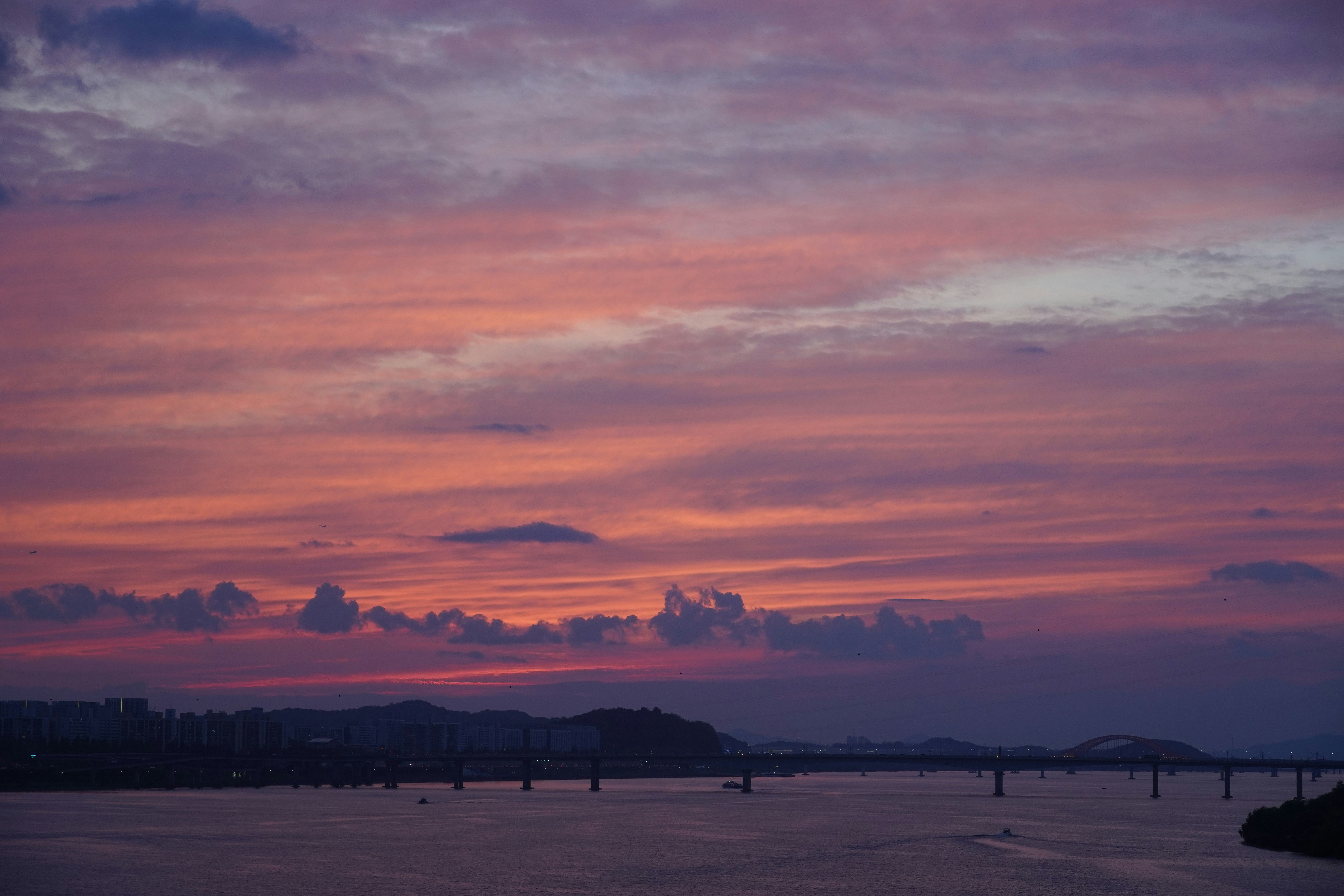 Vibrant sunset over a river with distant bridges.