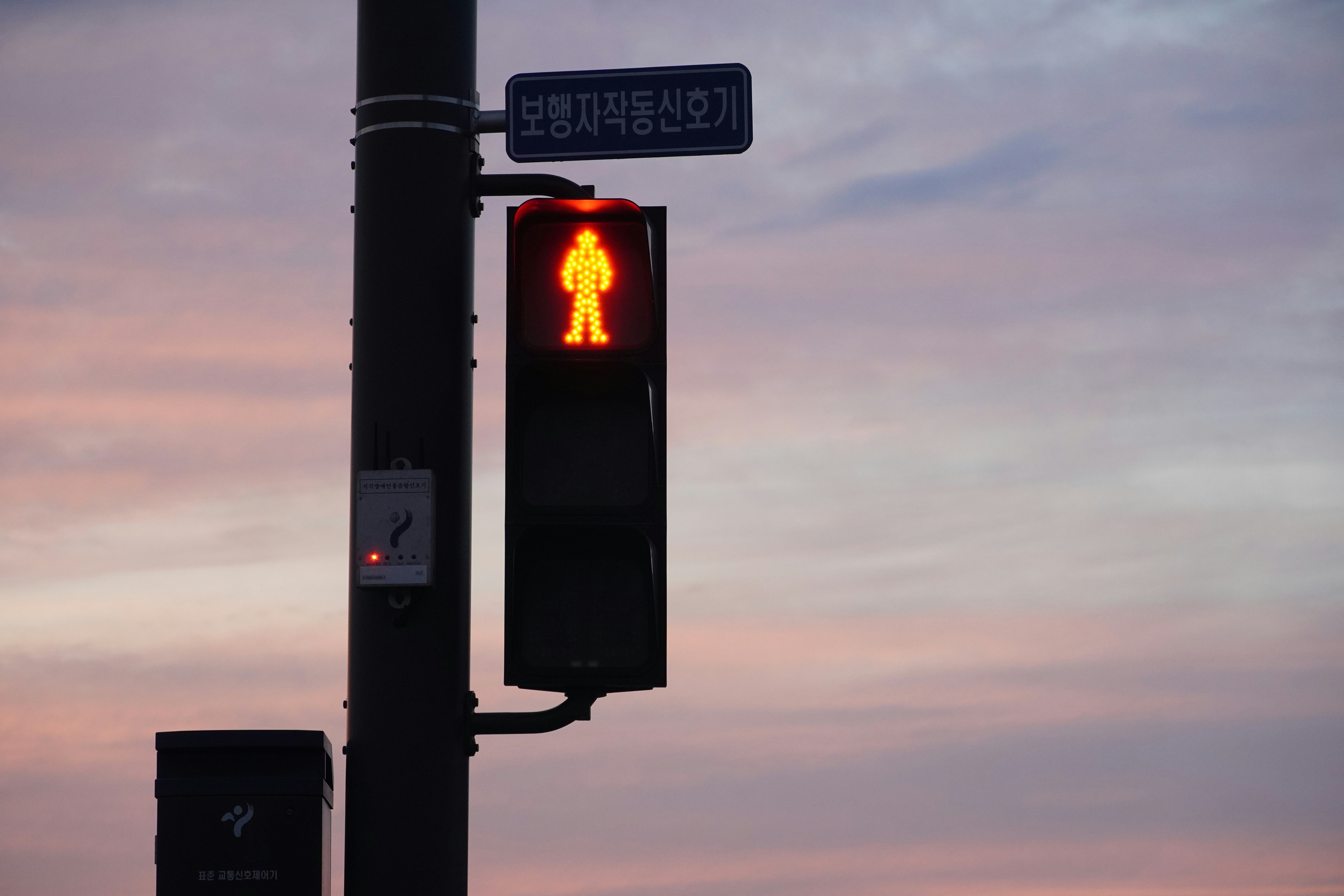 A red pedestrian traffic light against a colorful sunset sky.