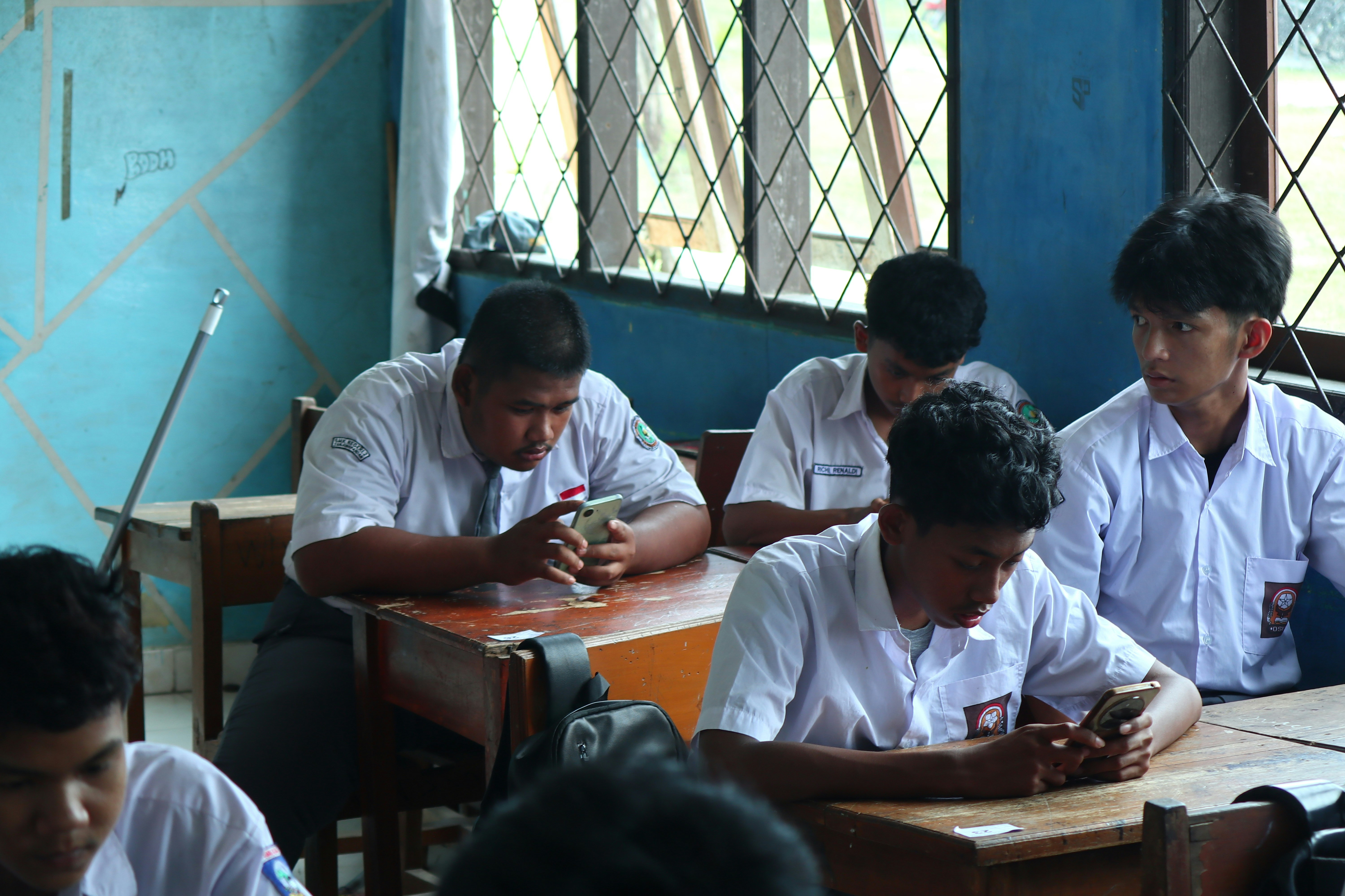 Students in uniform using phones in a classroom.