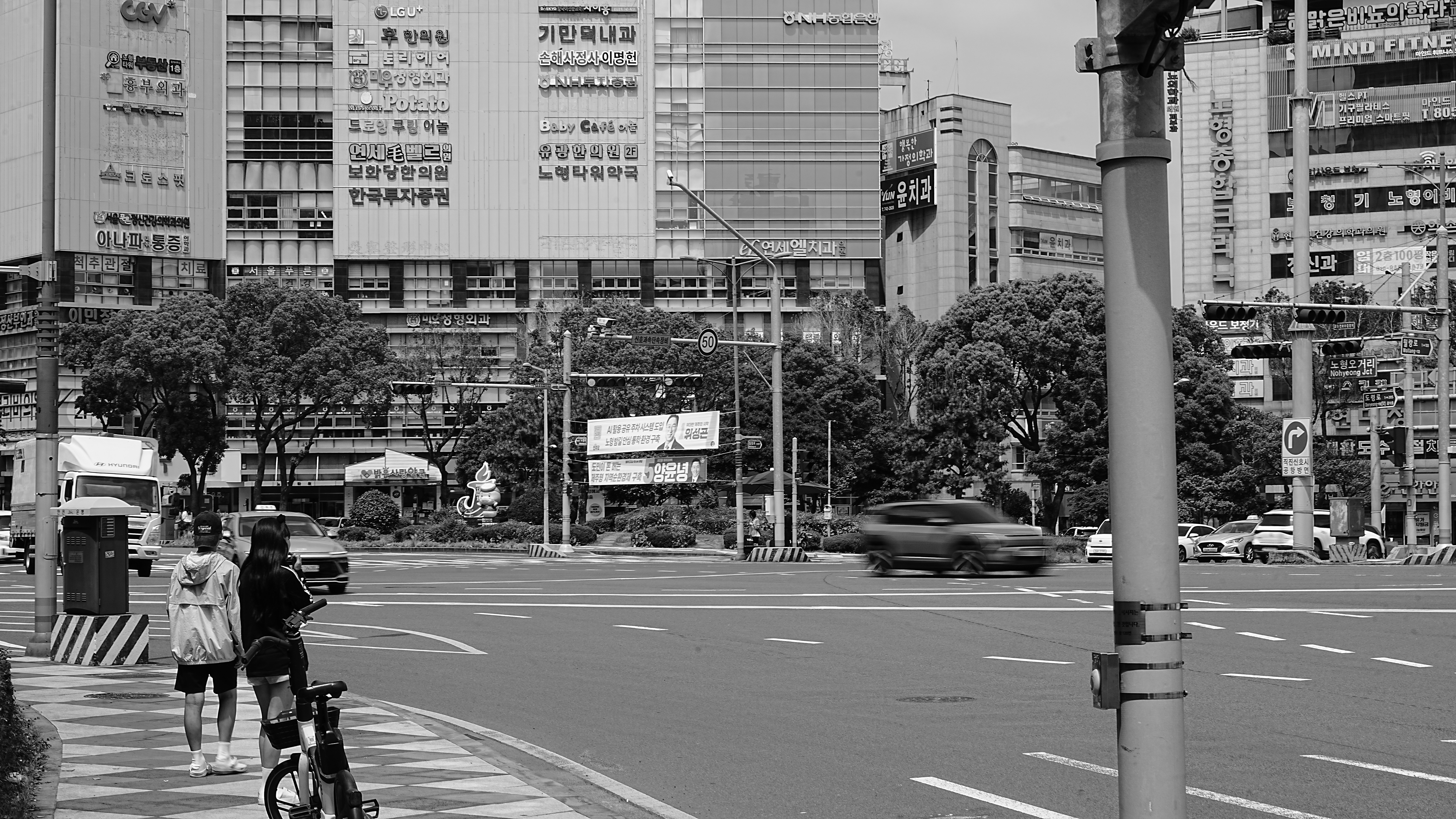 Black and white city street with people and moving car.