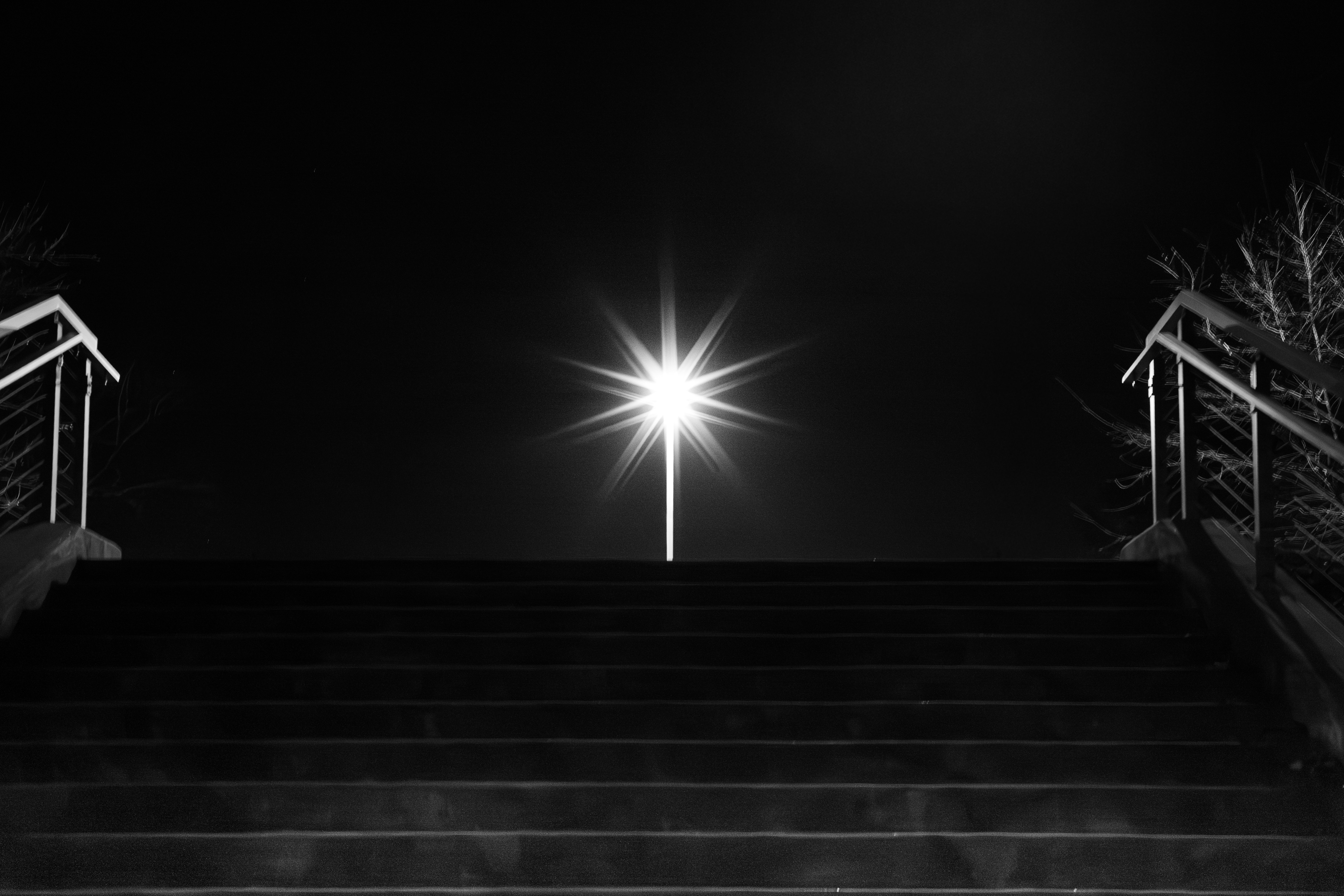 Dark stairs ascend towards a brilliant starburst light at night.