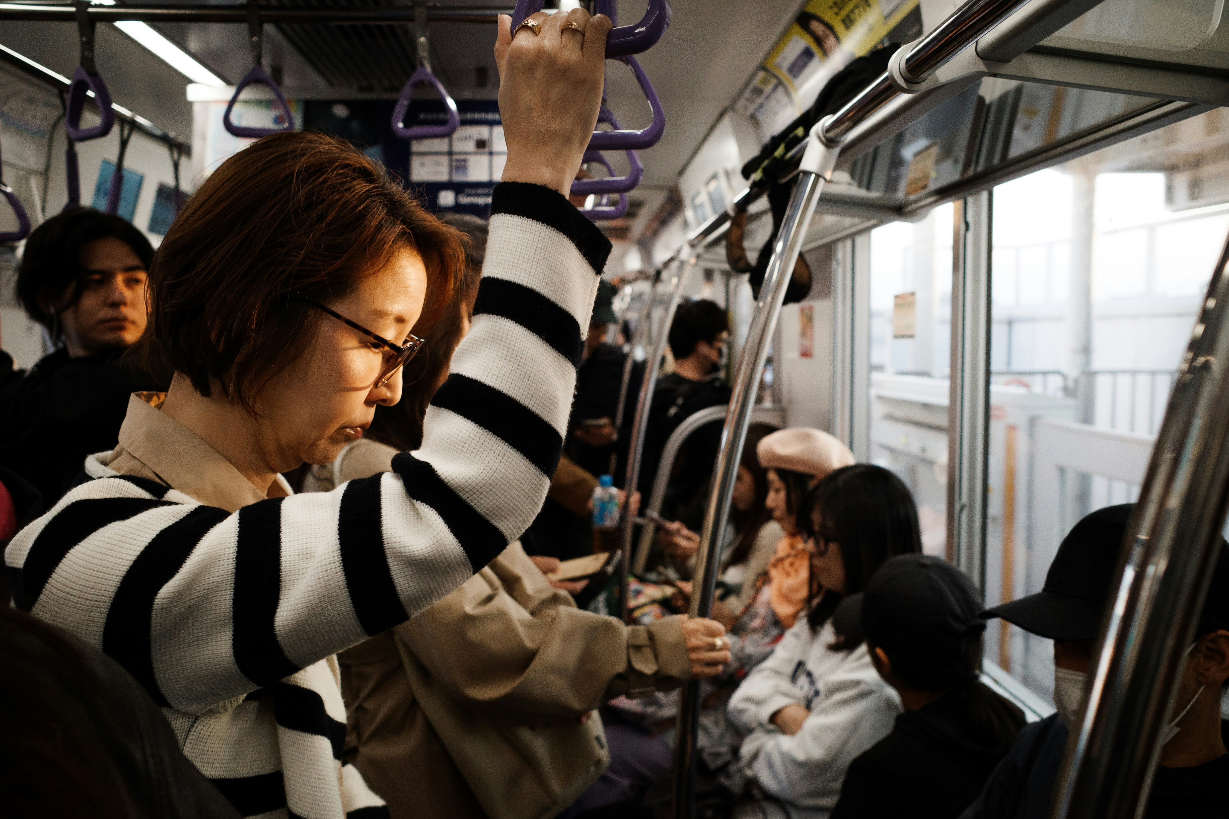 A woman stands holding a handrail inside a crowded train.