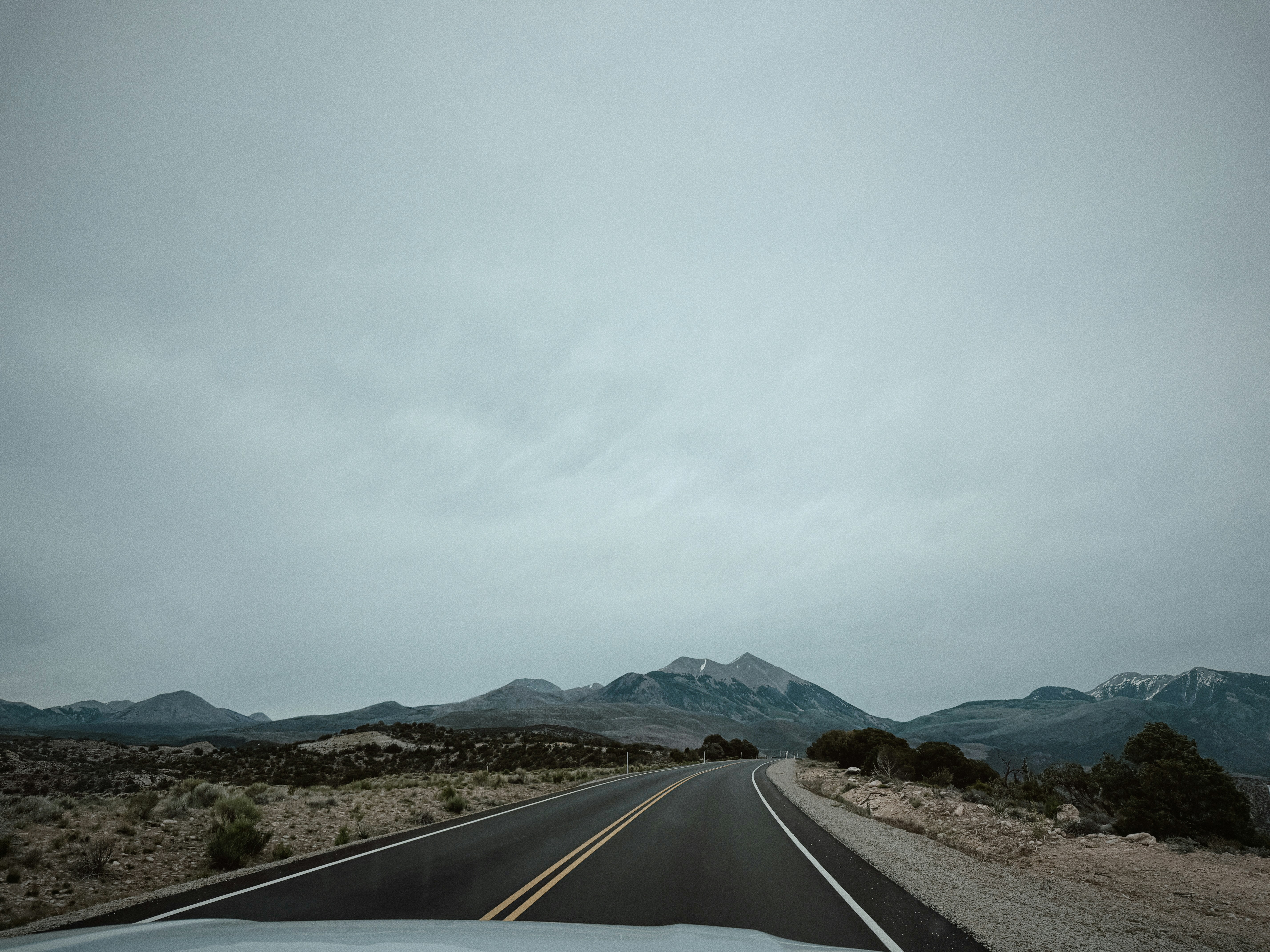 An empty road winds towards mountains under a gray sky.