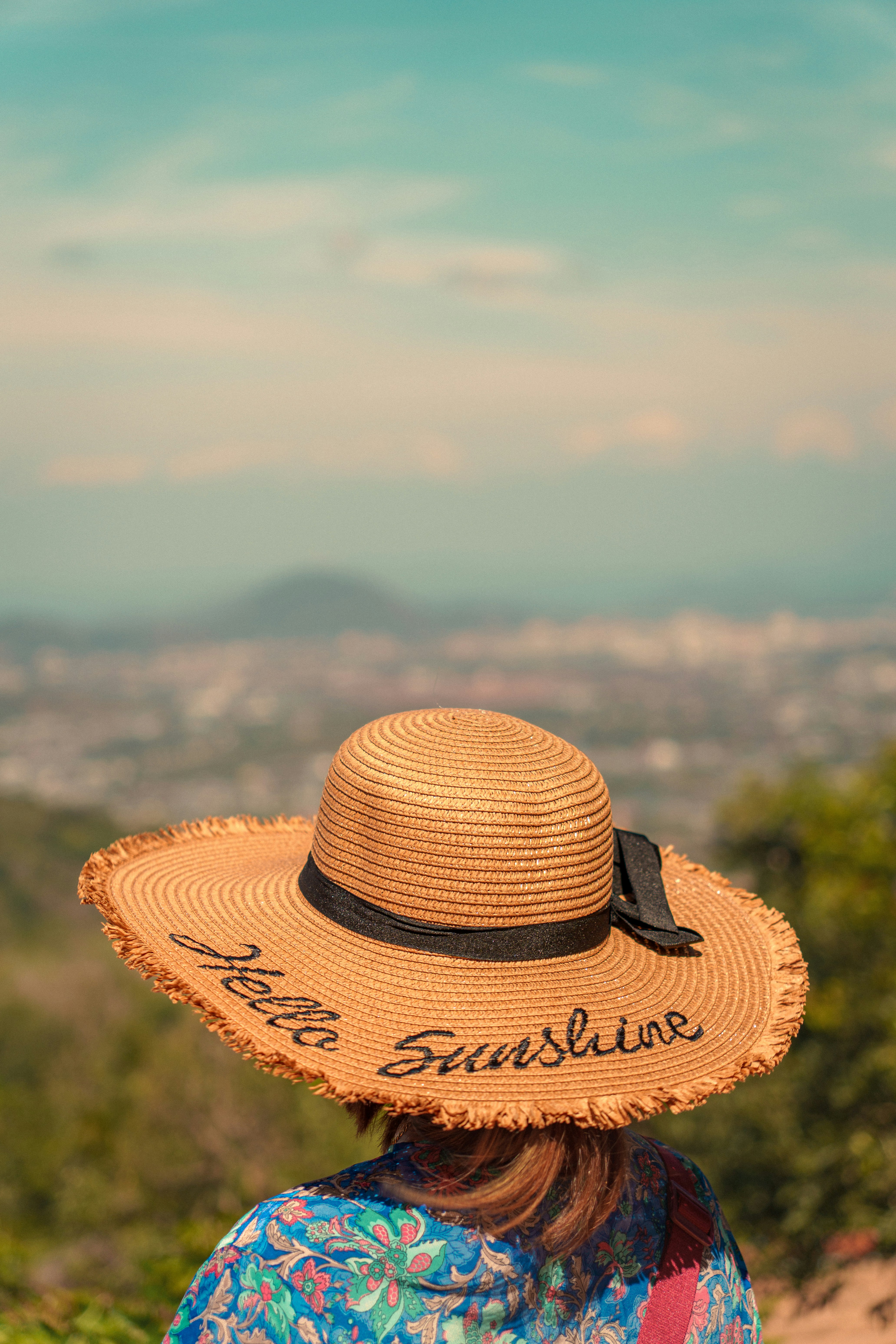 Sunlit Straw Hat with 'Hello Sunshine' Script Above a Distant Landscape