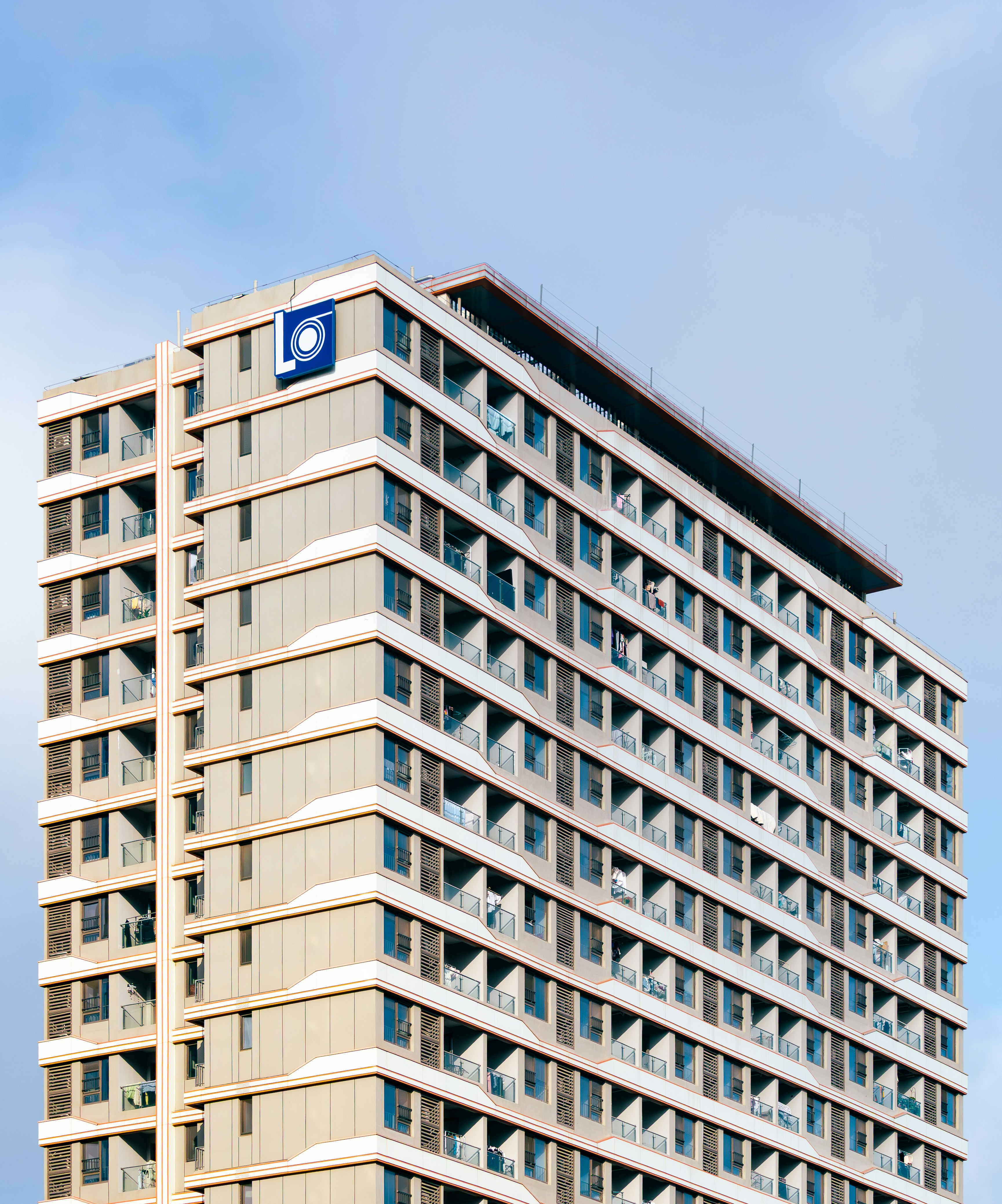 A modern high-rise building with balconies and a blue logo.