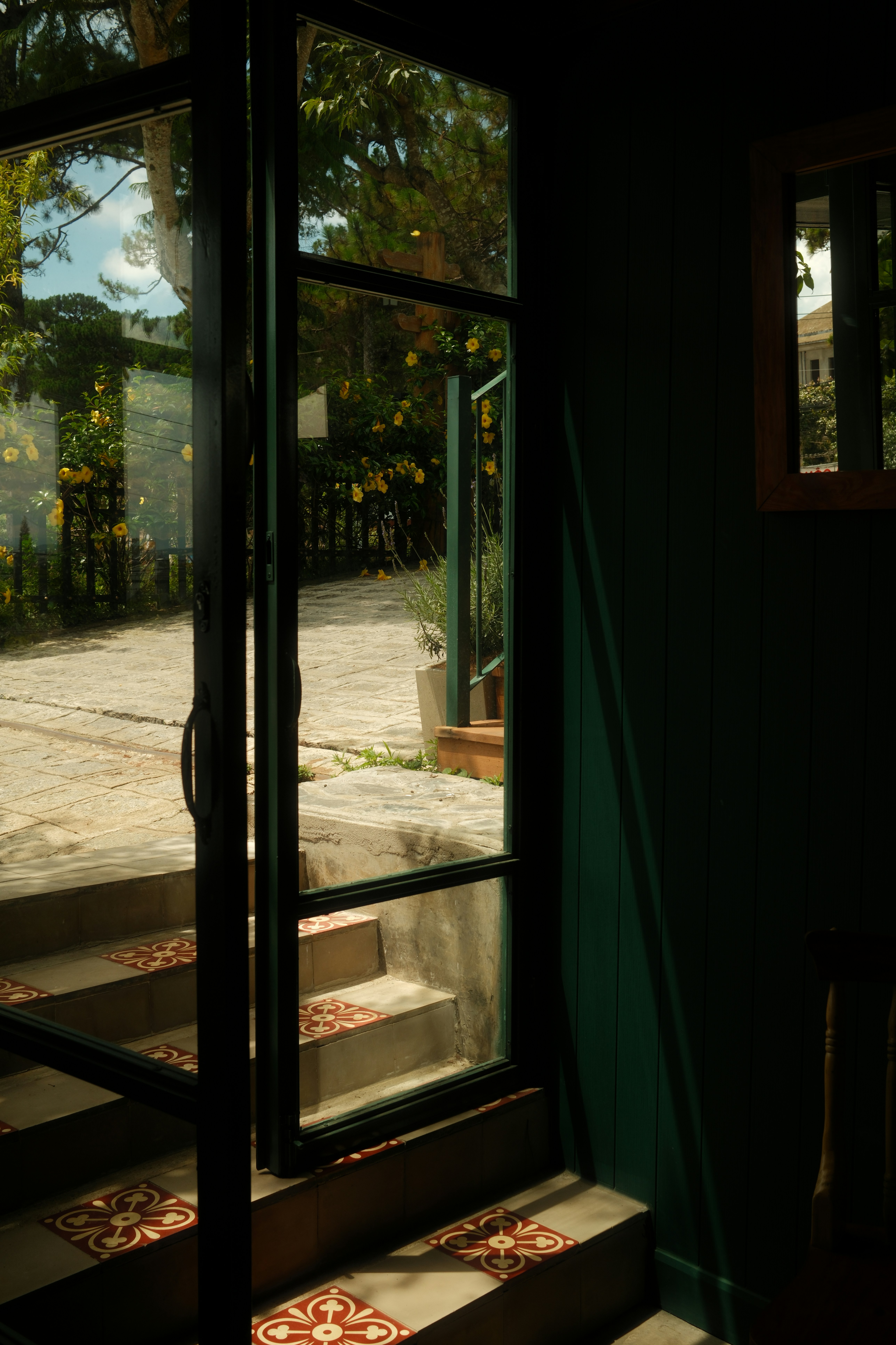 Open glass door revealing a bright garden and tiled stairs.
