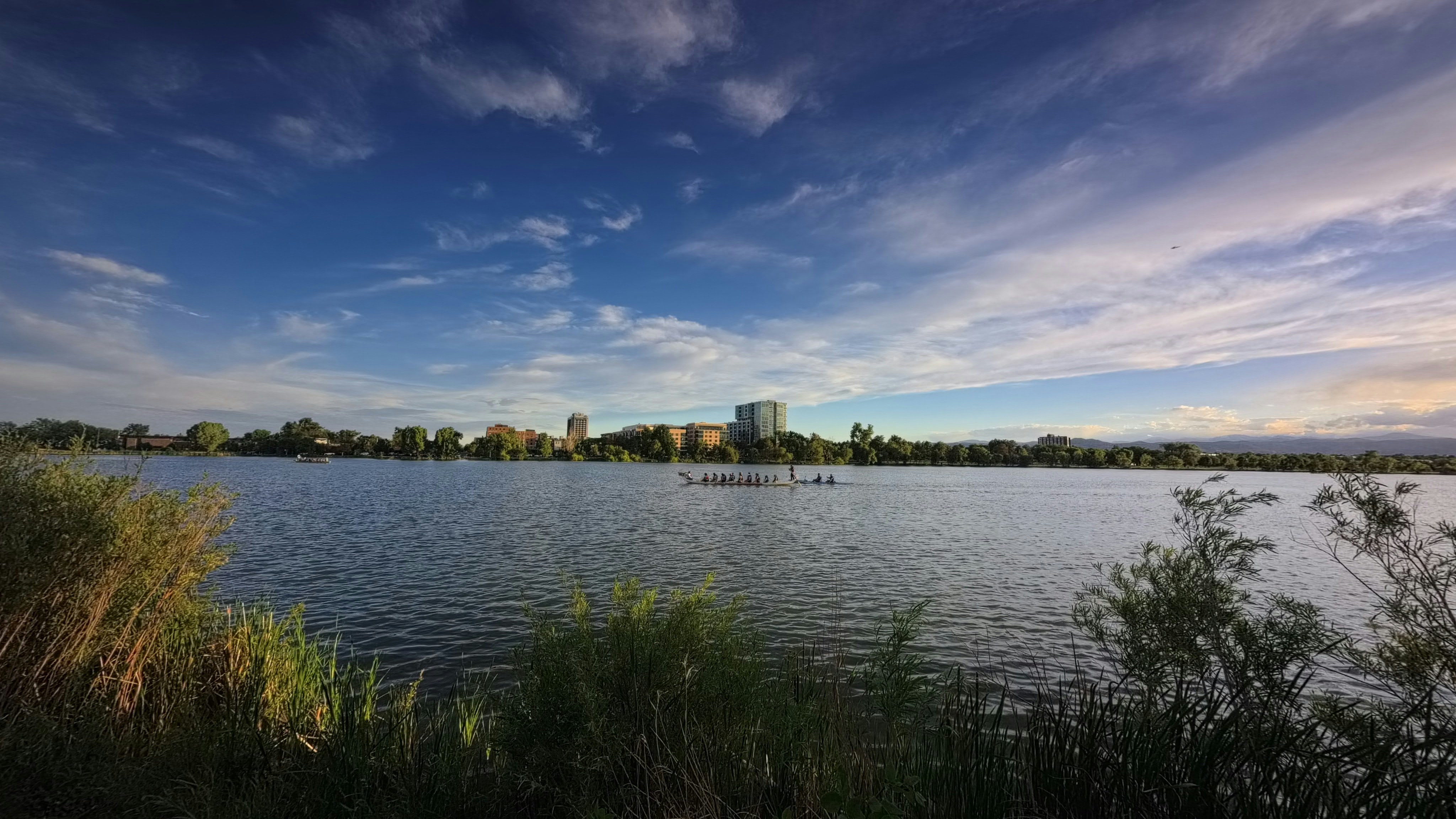 Scenic lake with distant cityscape under cloudy blue sky.