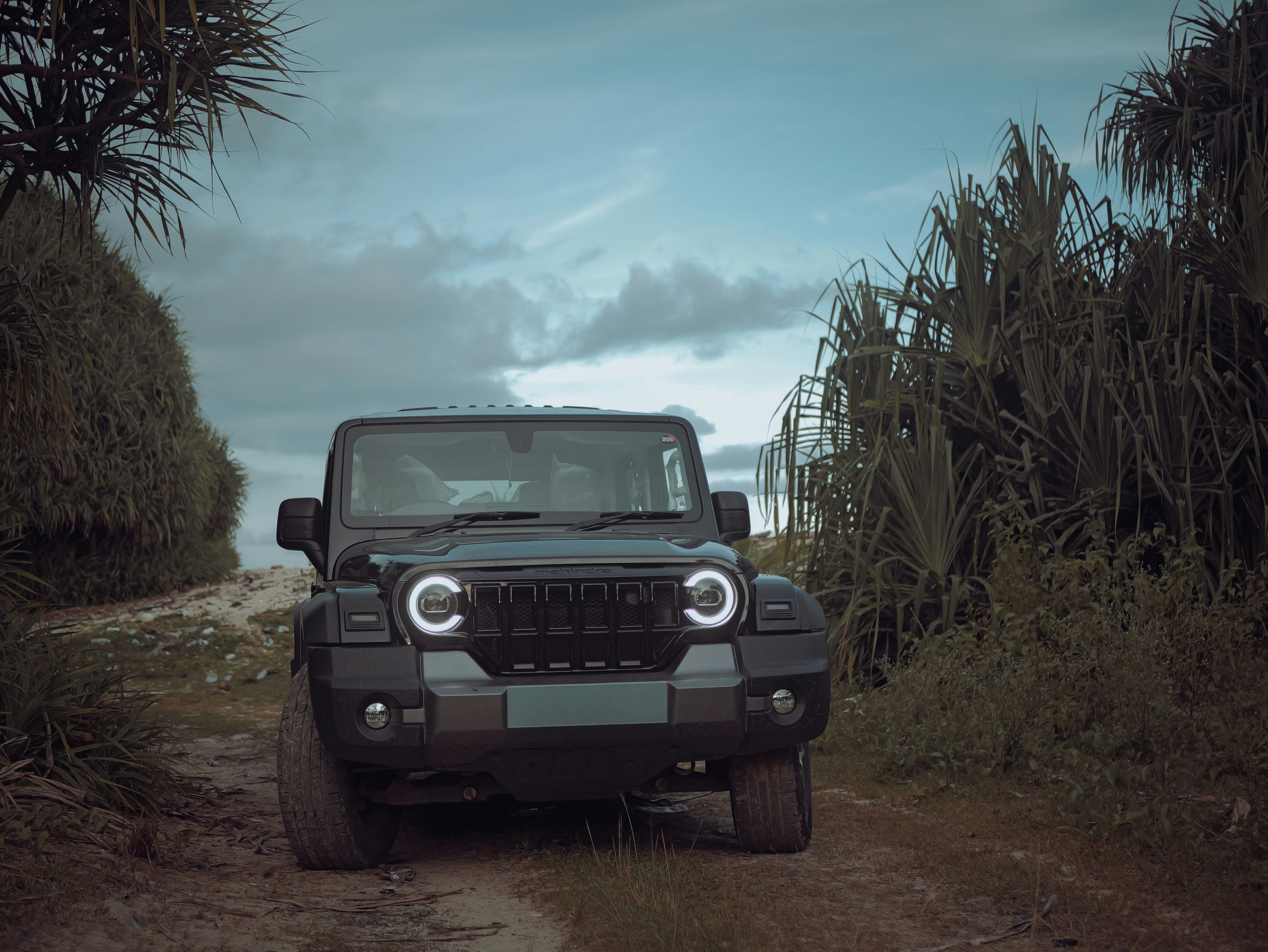 A dark suv with circular headlights on a dirt road.