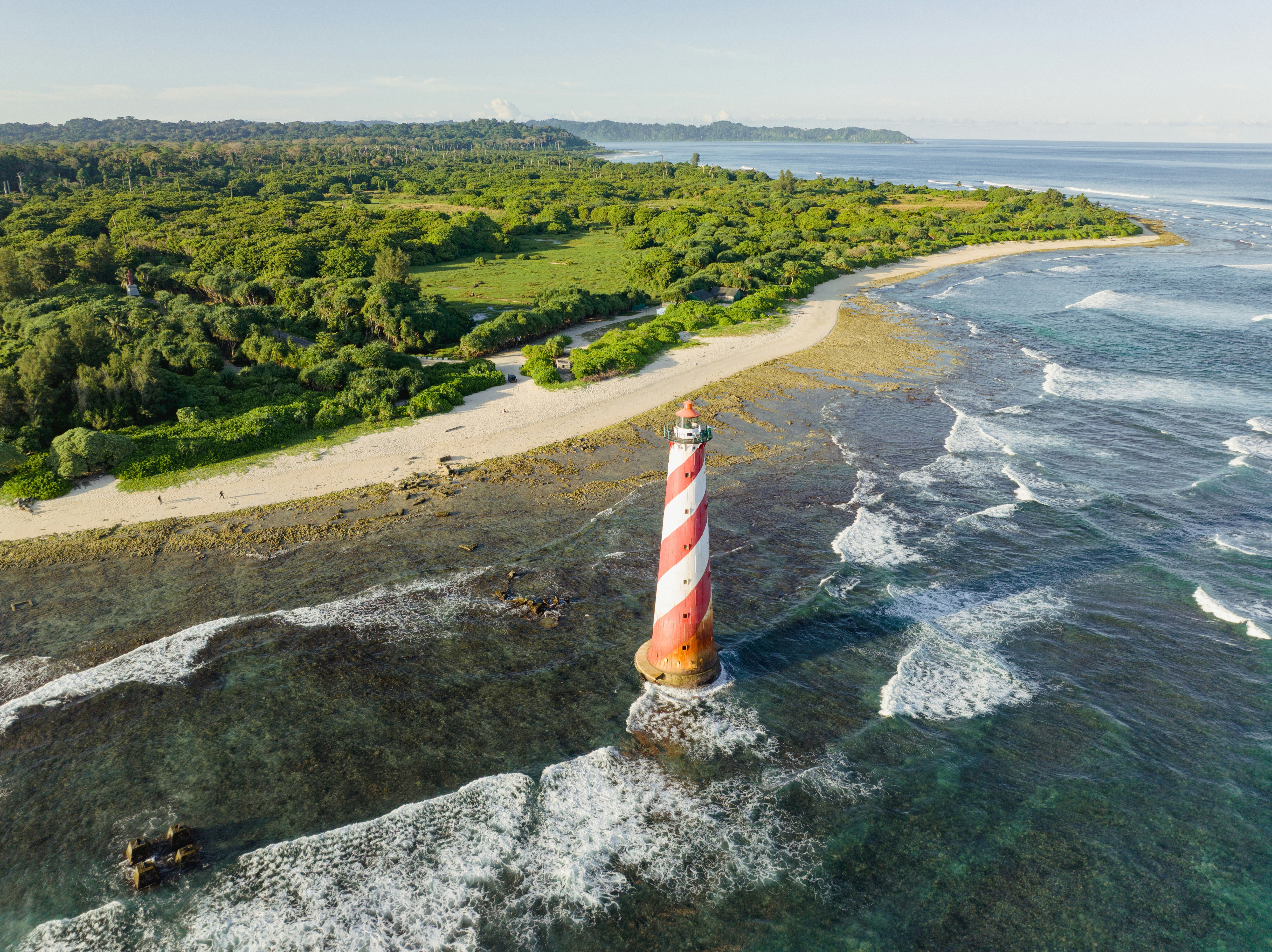 Red and white striped lighthouse in ocean near green island.