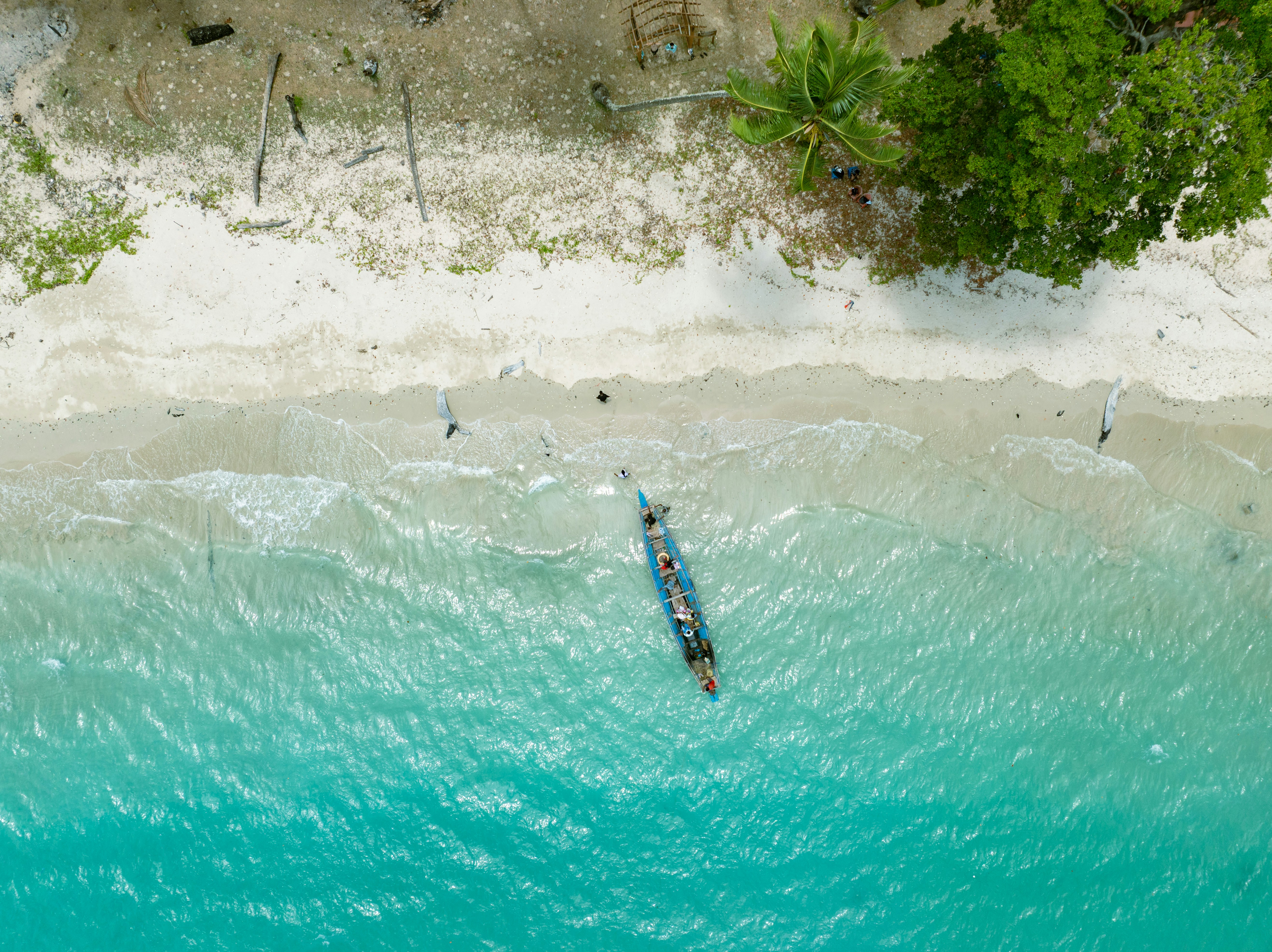 Boat floats on clear turquoise water beside a white beach.