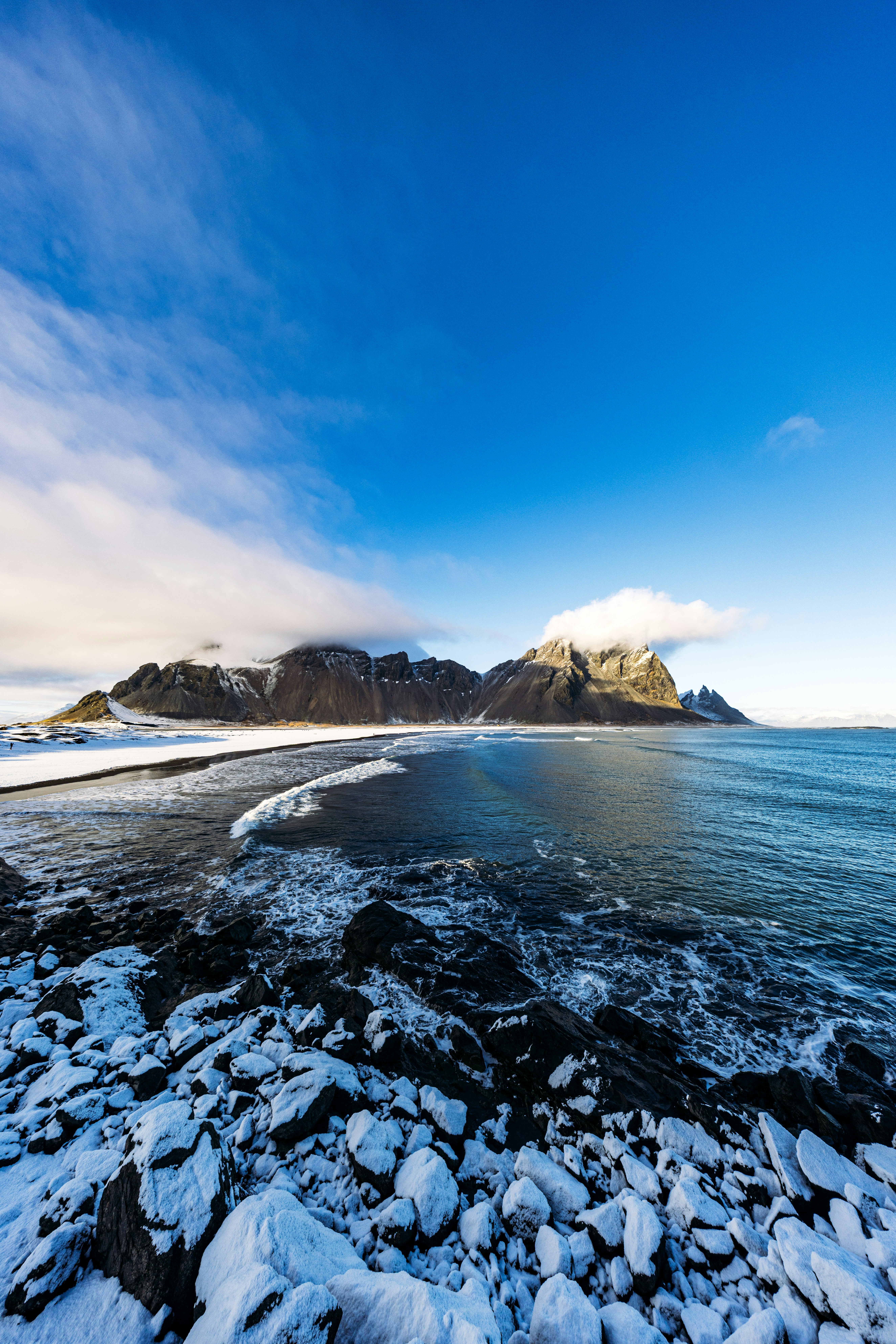 Snowy coastline with mountains and ocean under a blue sky.