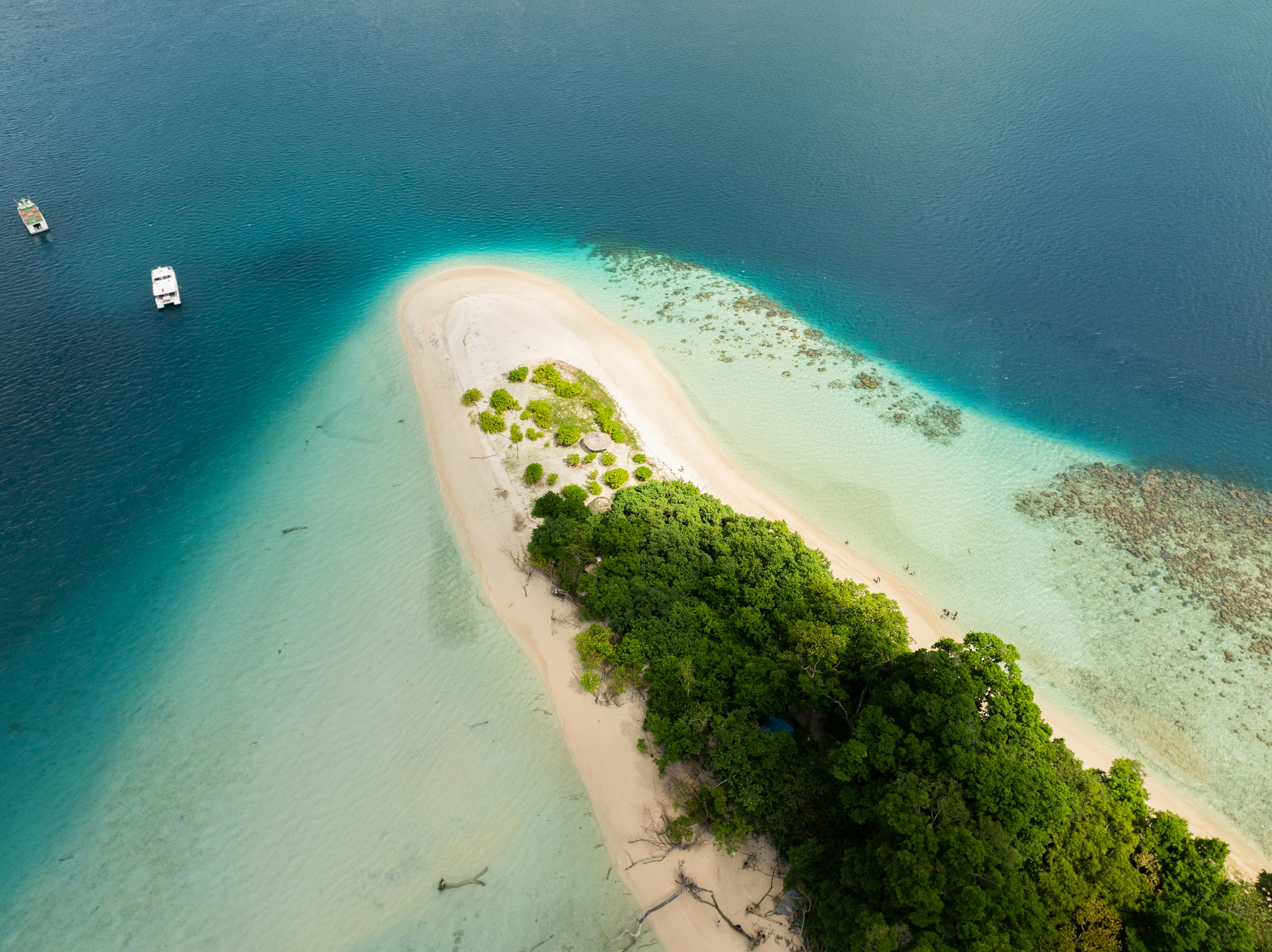 Sandy island spit with tropical trees and clear blue ocean.