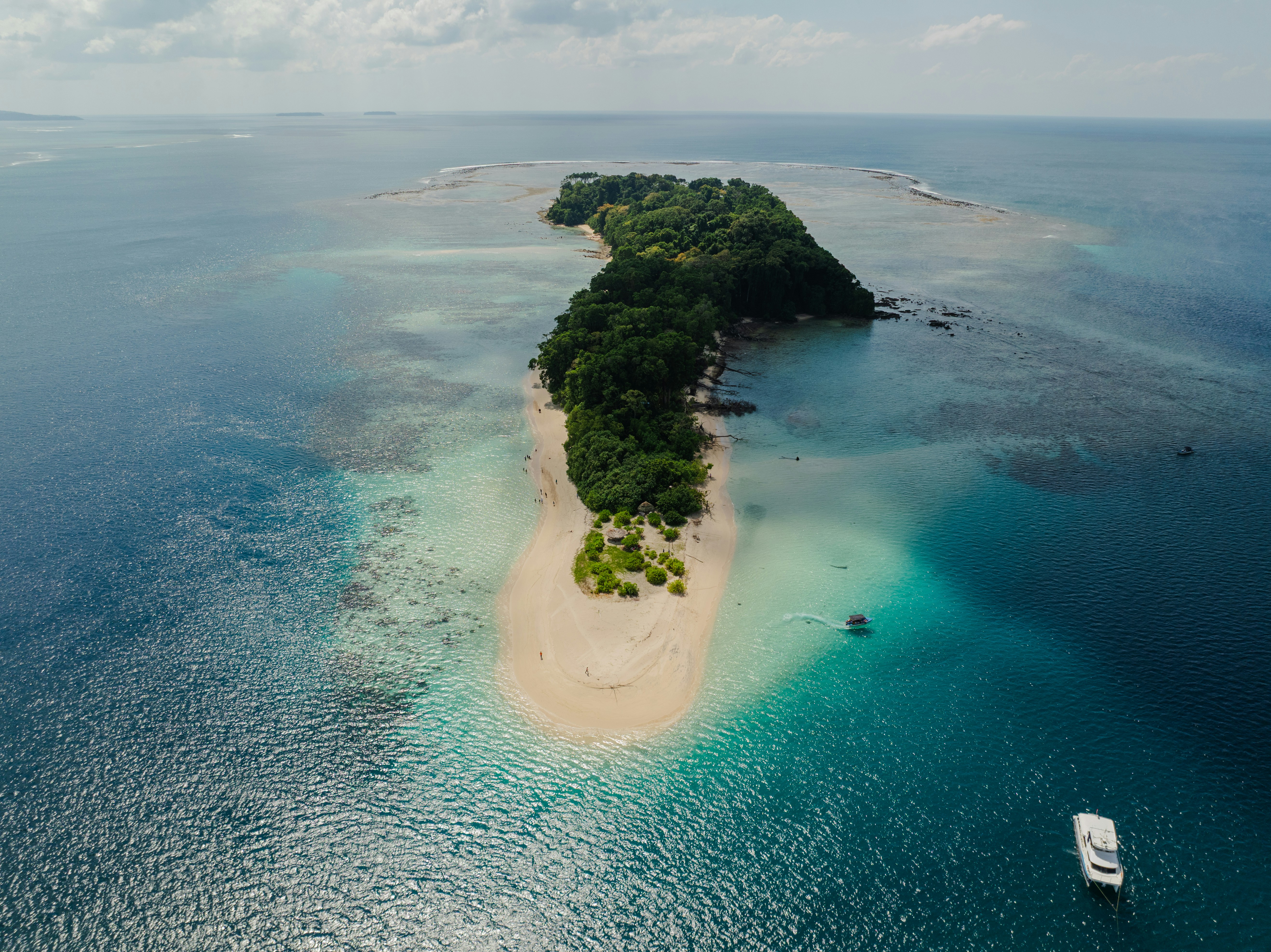Tropical island with sandy beach, turquoise ocean, and white boat.