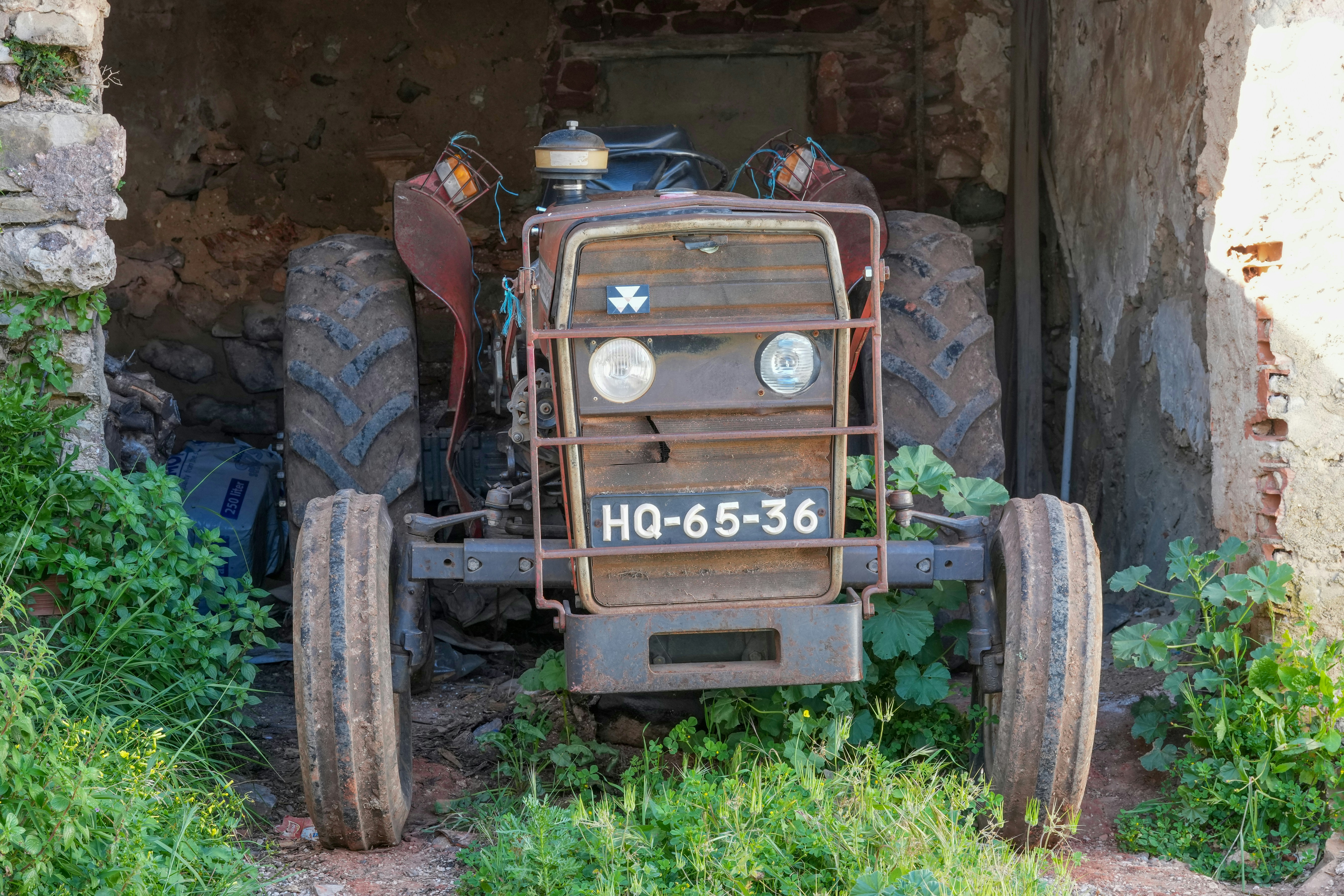 Old rusty tractor parked inside a rustic stone building.