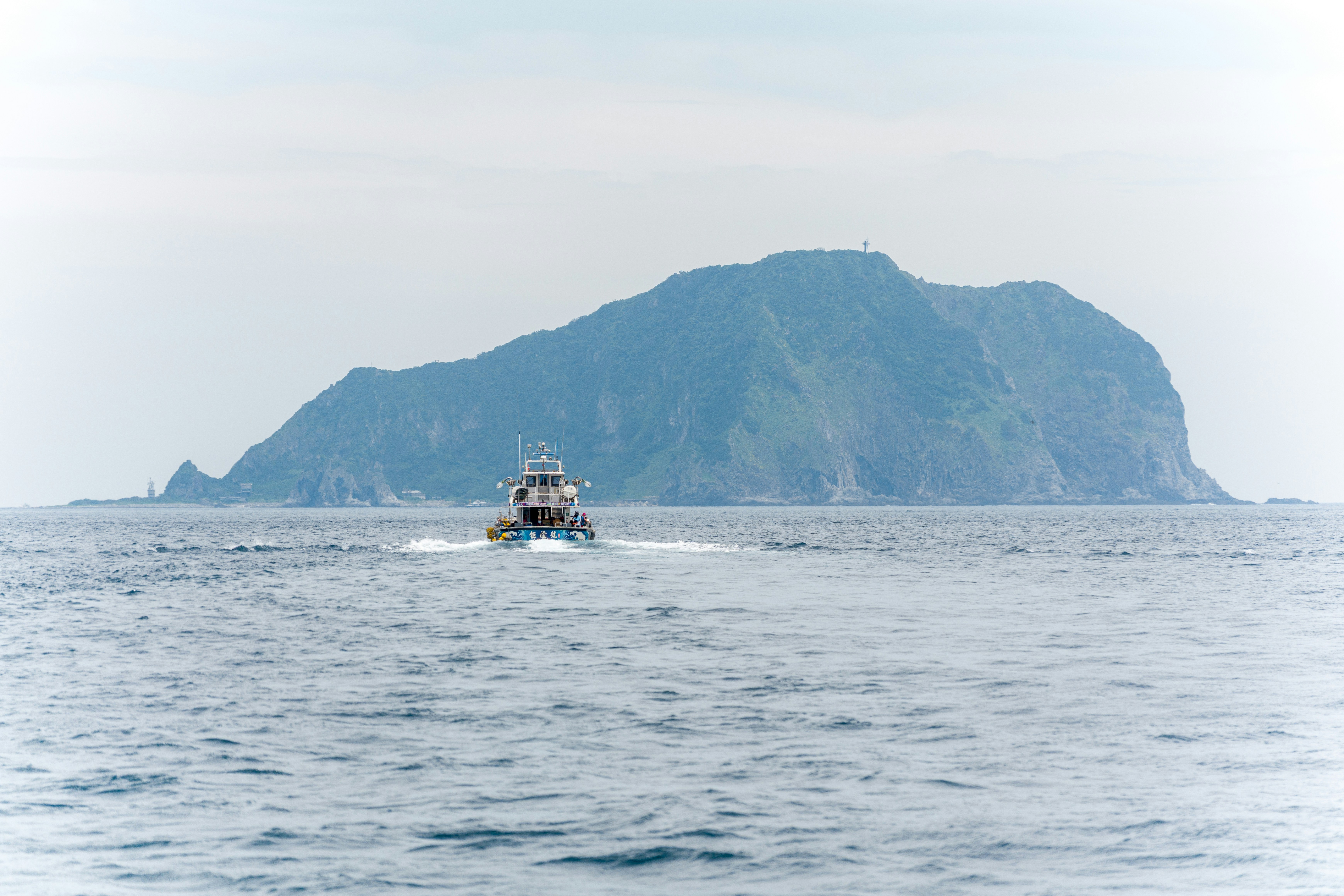 Boat approaching a large, rocky island in the ocean.