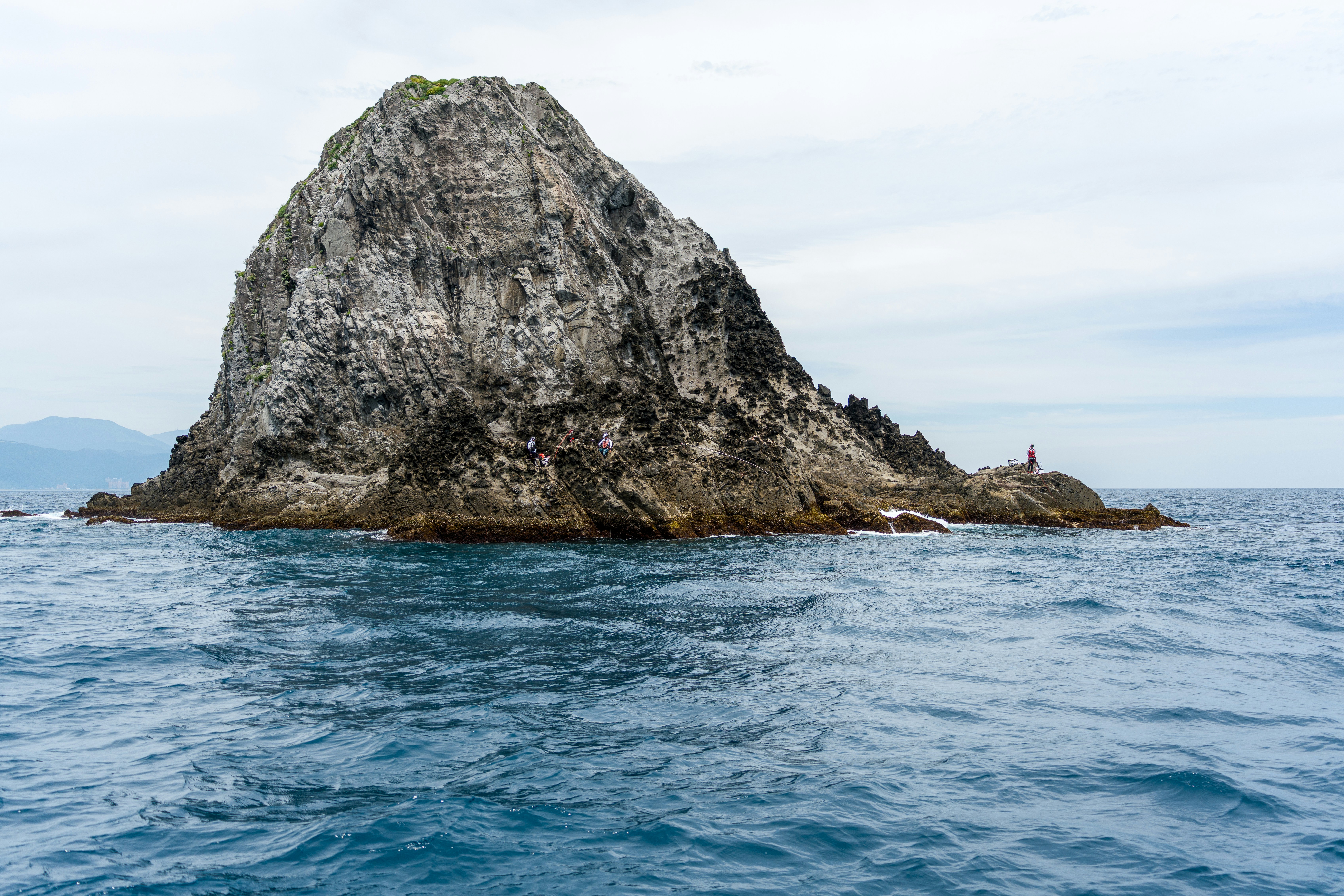 Rocky island with beacon in blue ocean under cloudy sky.
