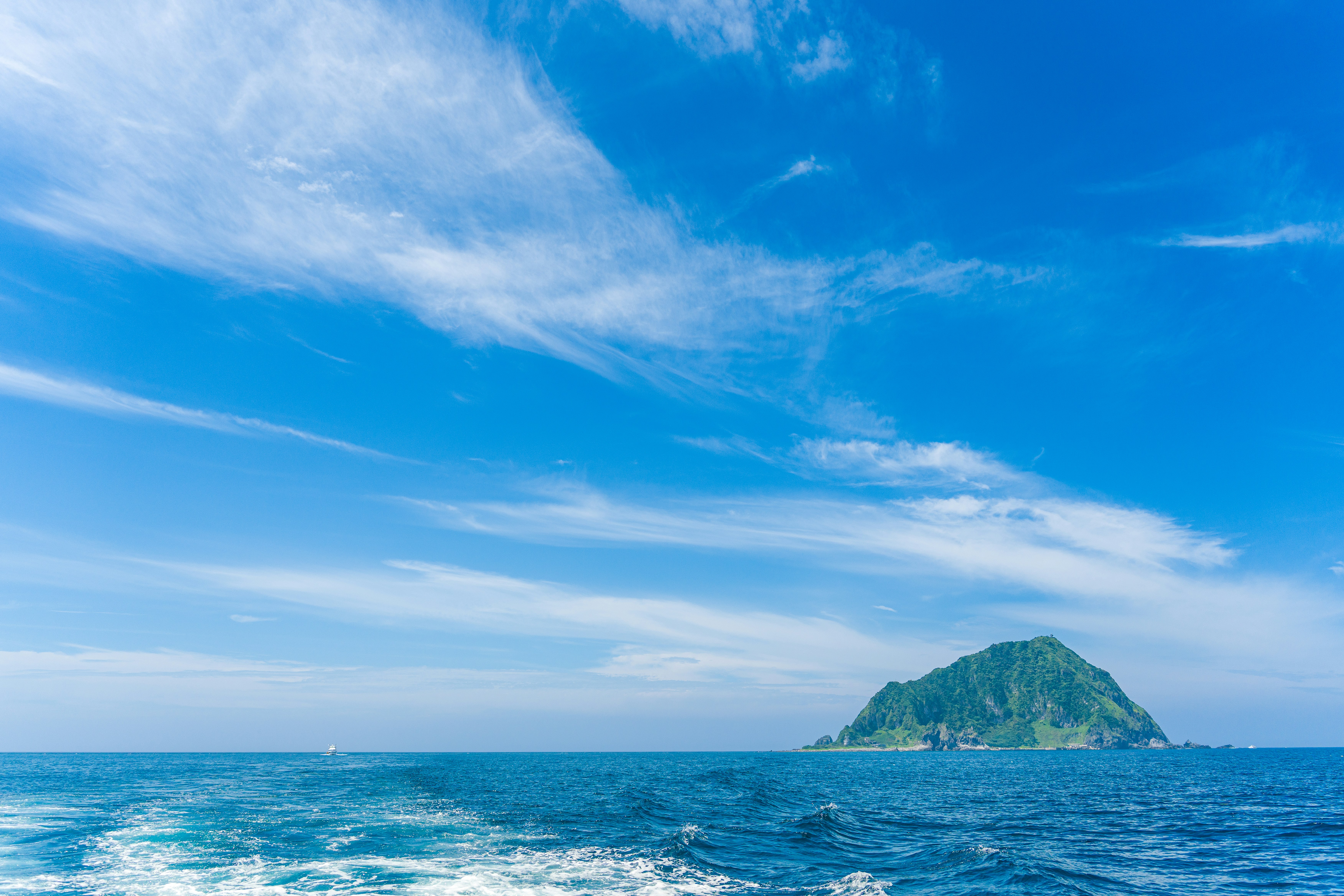 Distant green island in a blue ocean and sky.