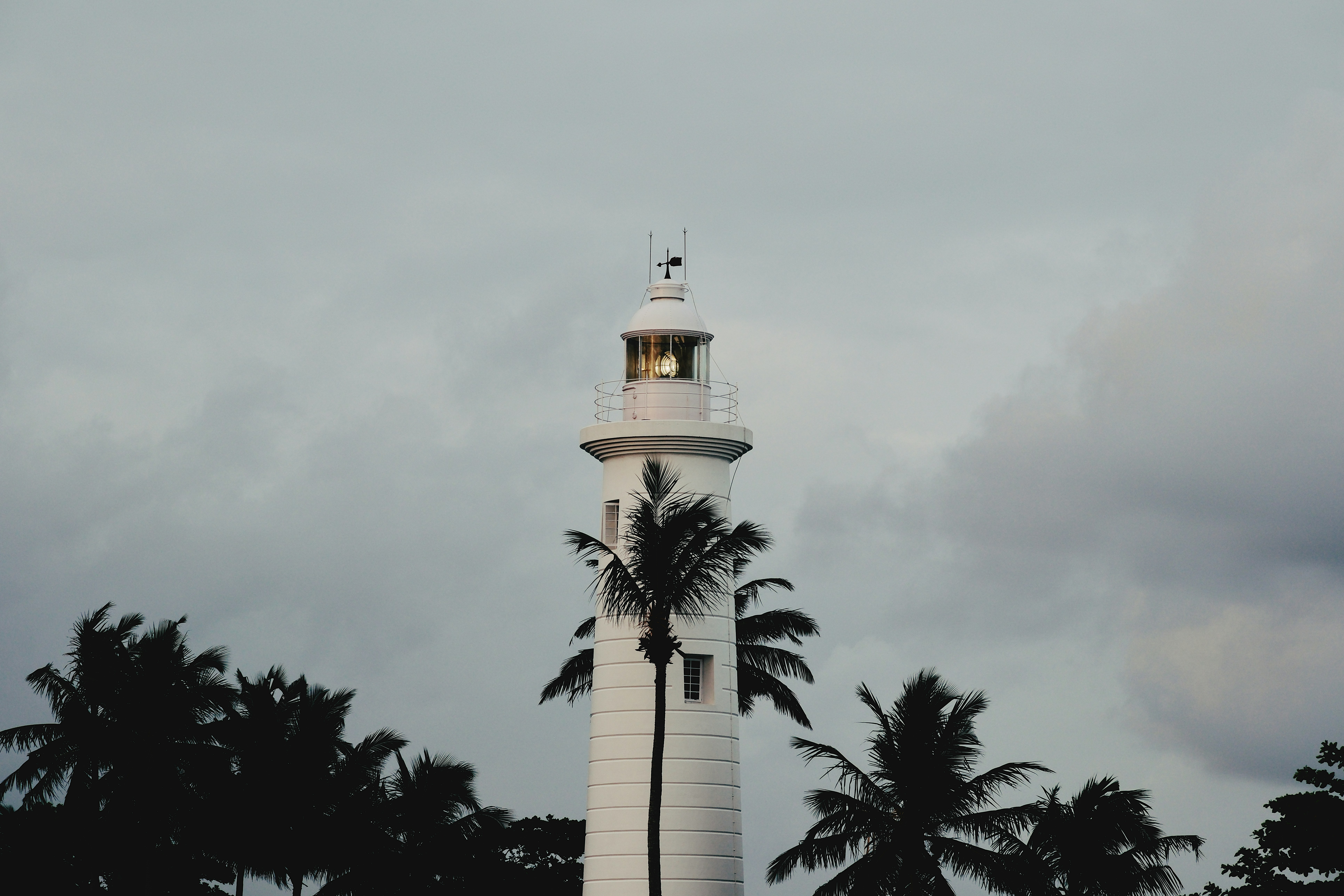 A lone beacon rises above the palms, holding its light against the gathering clouds. ⸻ Fujifilm X-T5 • 81.3mm • ƒ/9