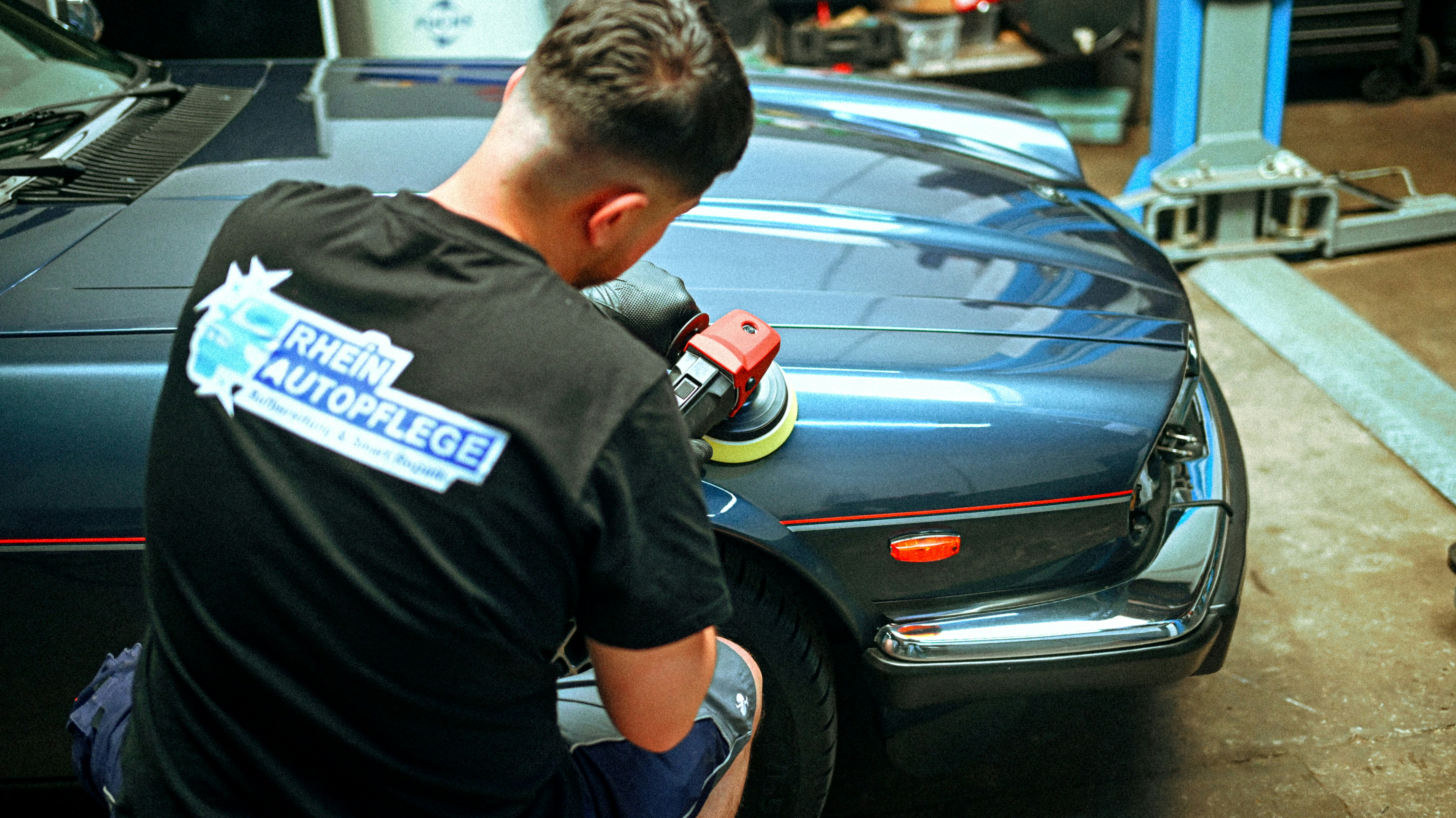 A person polishing a blue vintage car in a workshop.