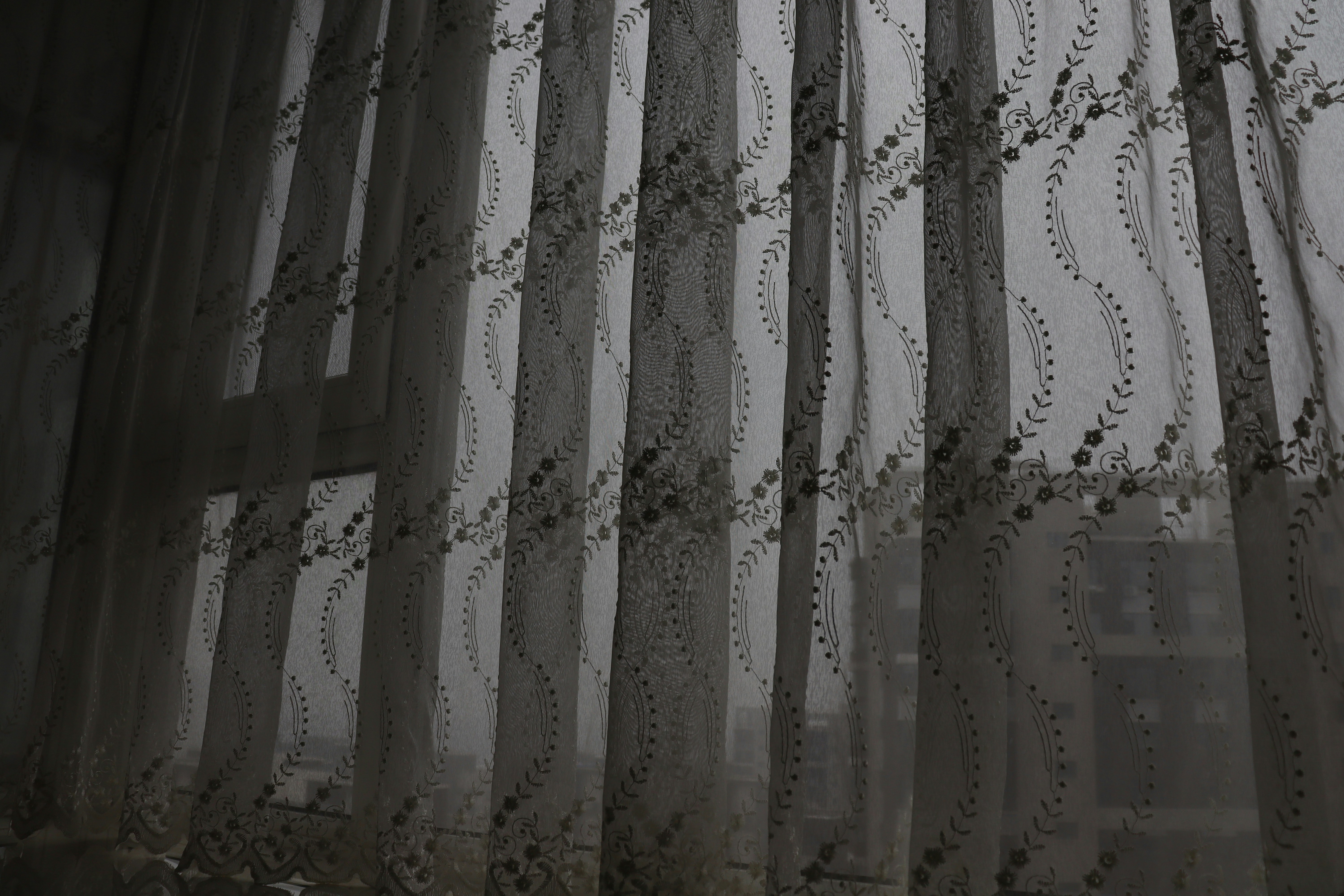 Dark sheer curtains with a subtle pattern over a window.