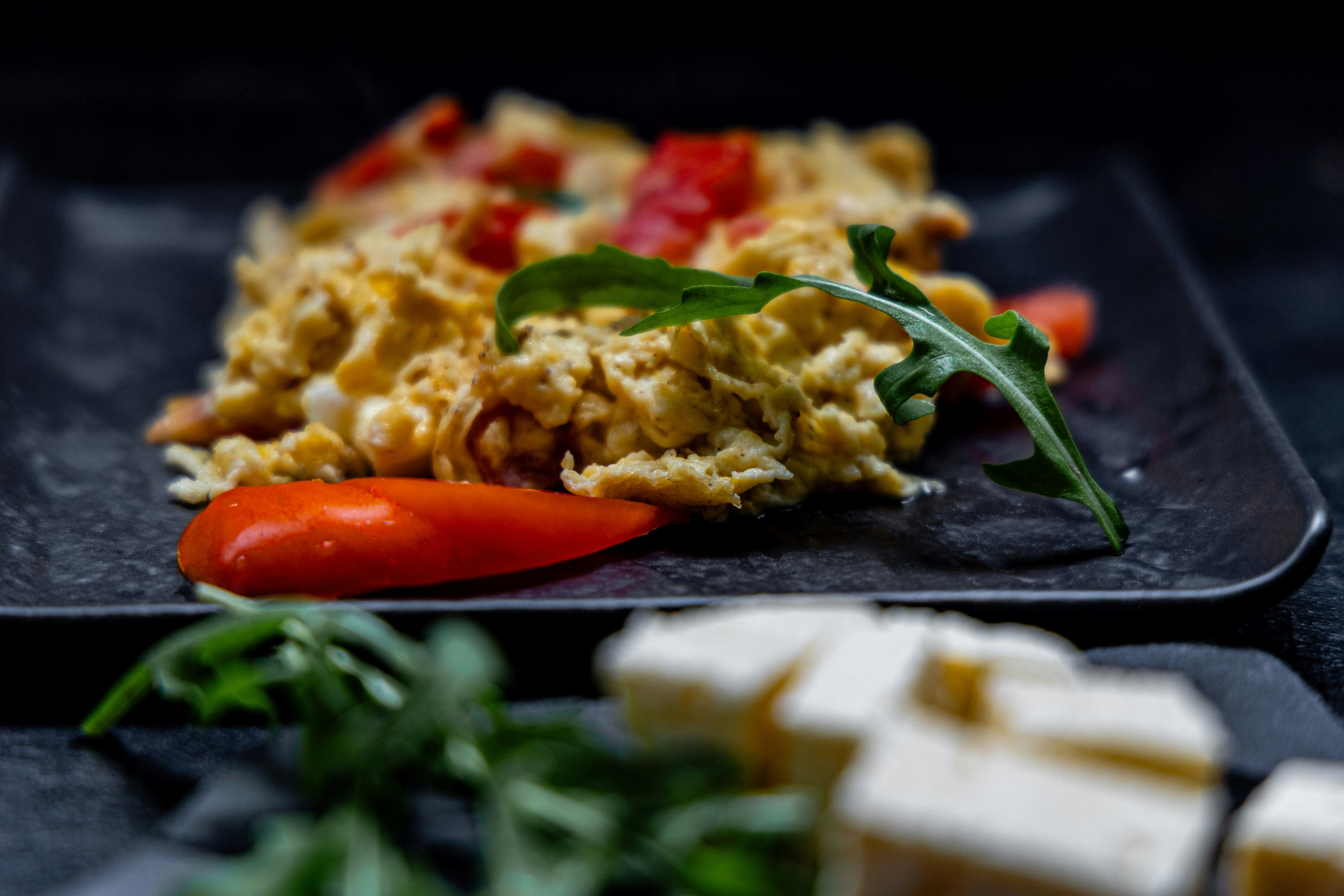 Scrambled eggs with tomatoes and arugula on a dark plate.