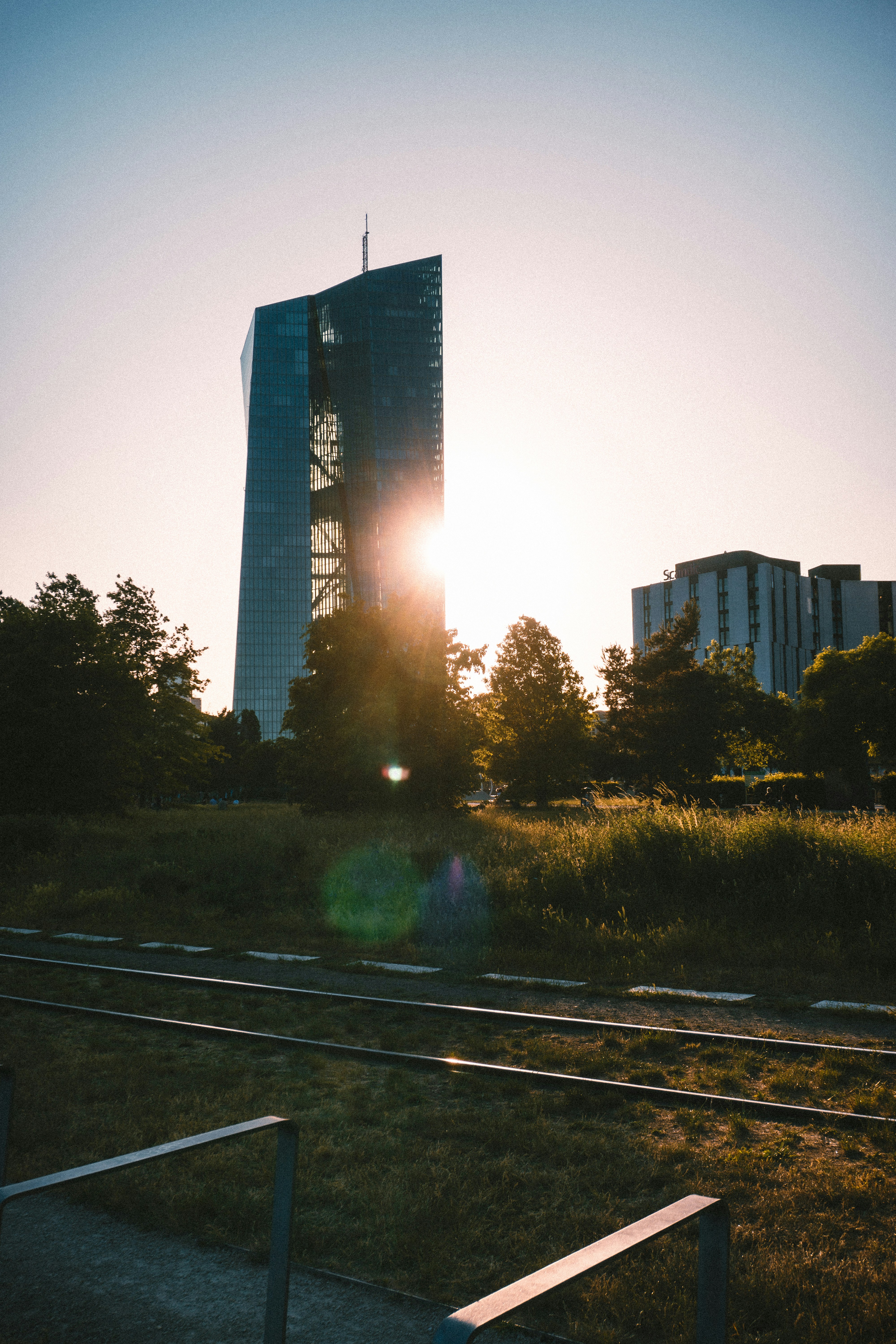 Sunlit Edge: A Skyscraper Glows Over Train Tracks at Dusk