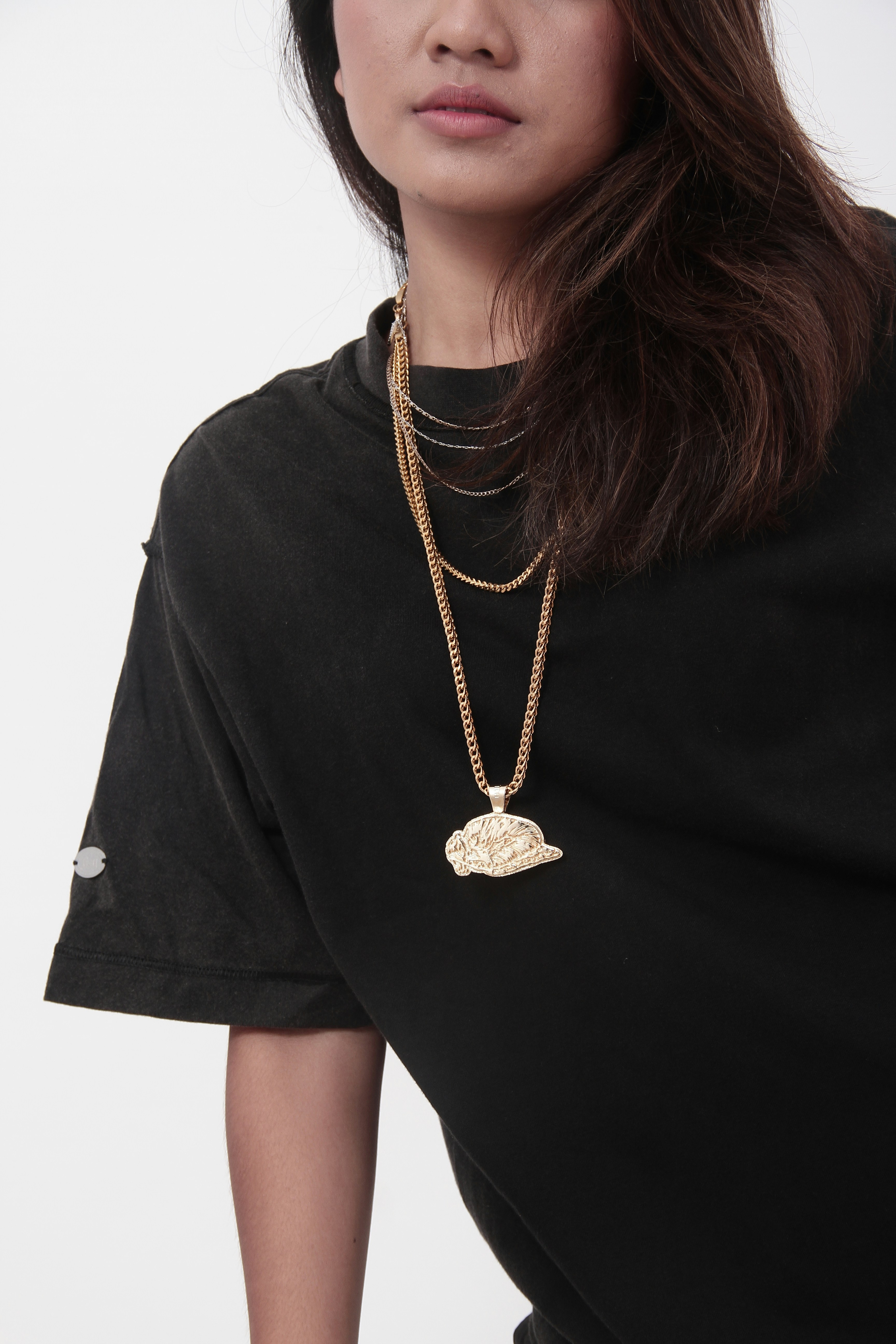 Gold pendant over a black tee: close-cropped portrait with layered chains