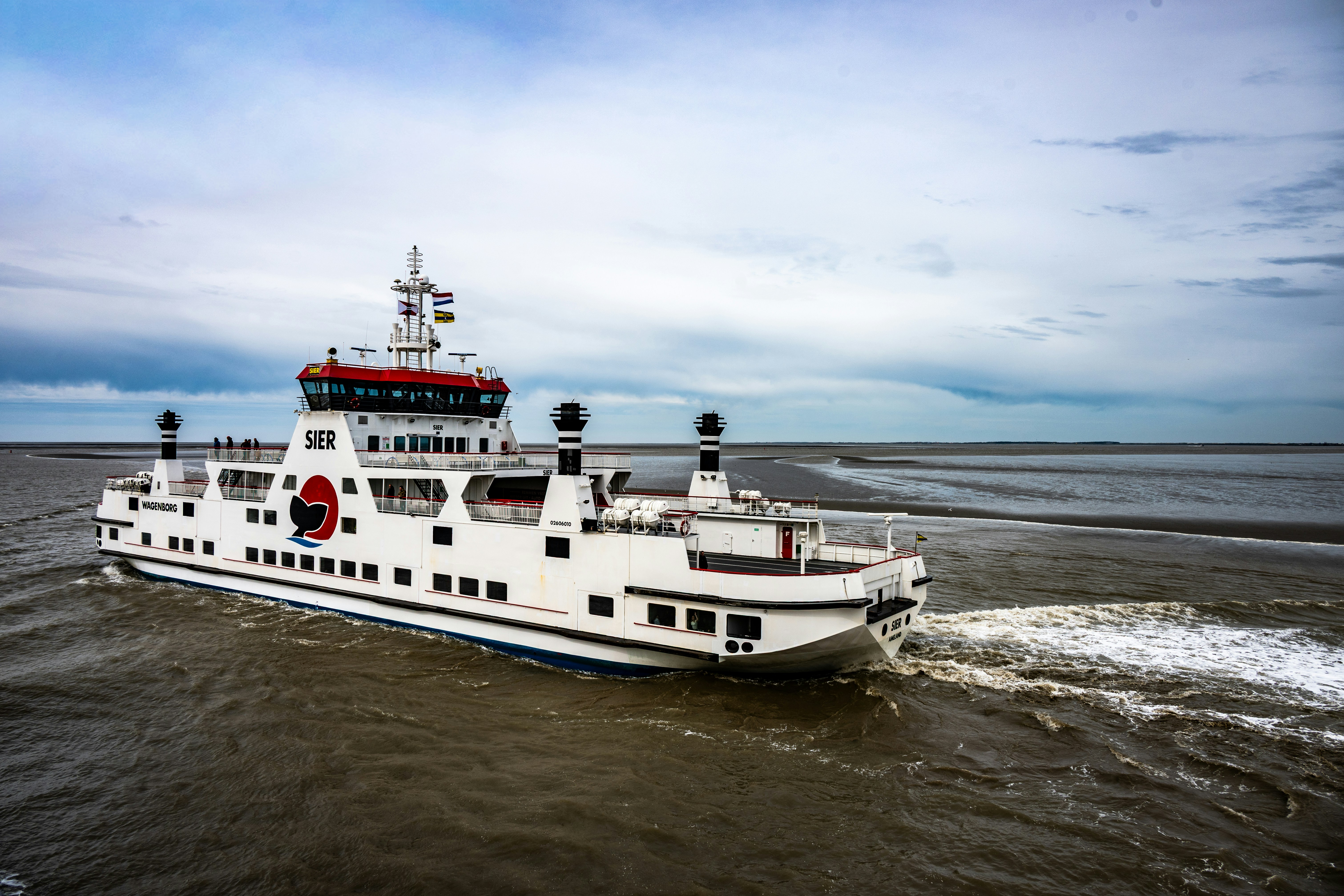 Large white ferry sails through shallow, muddy water.