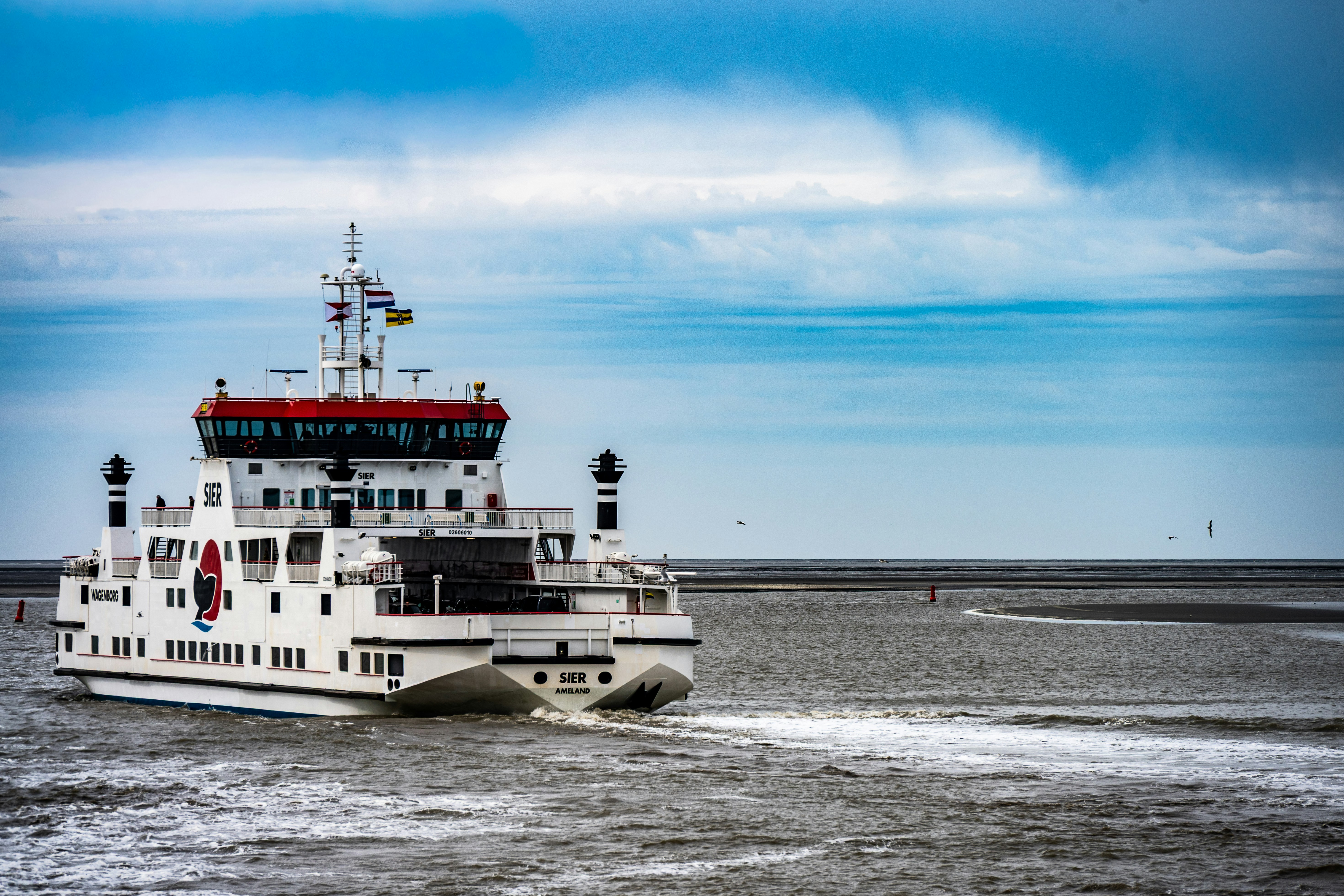 Large white ferry sailing away on calm water.
