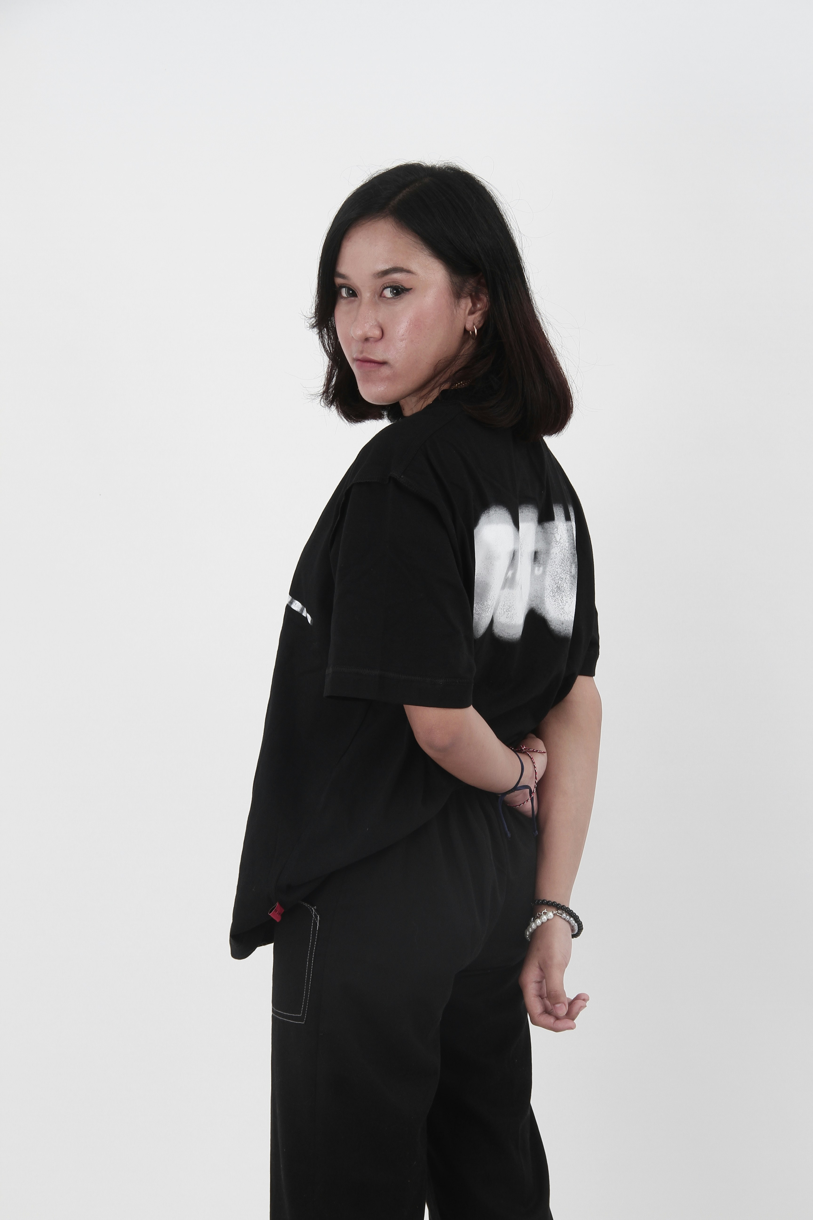 Portrait of a neutral-eyed woman in a black outfit standing with her back slightly turned in a clean studio setting.
