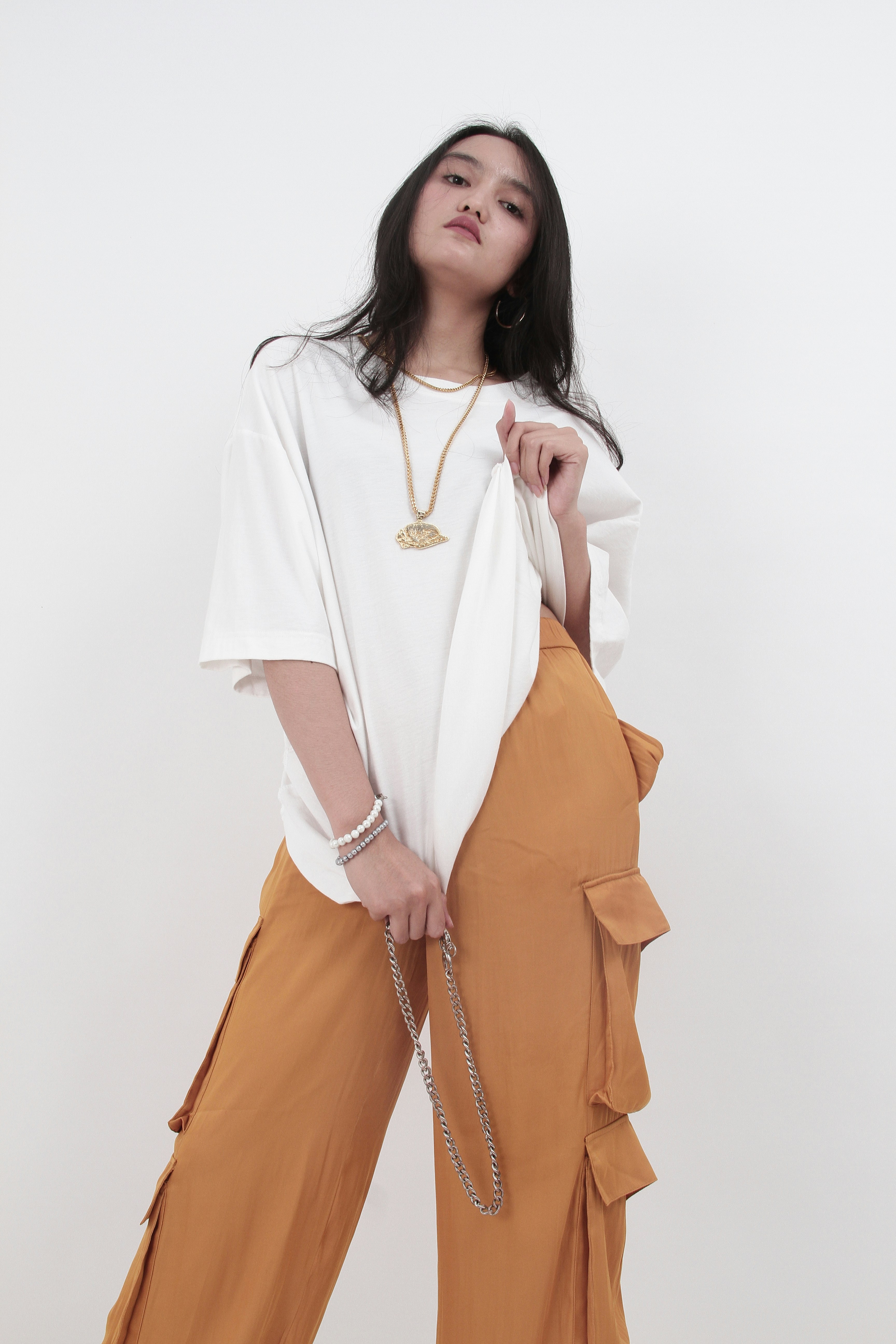 White tee, amber cargo pants: a relaxed studio pose with bold jewelry