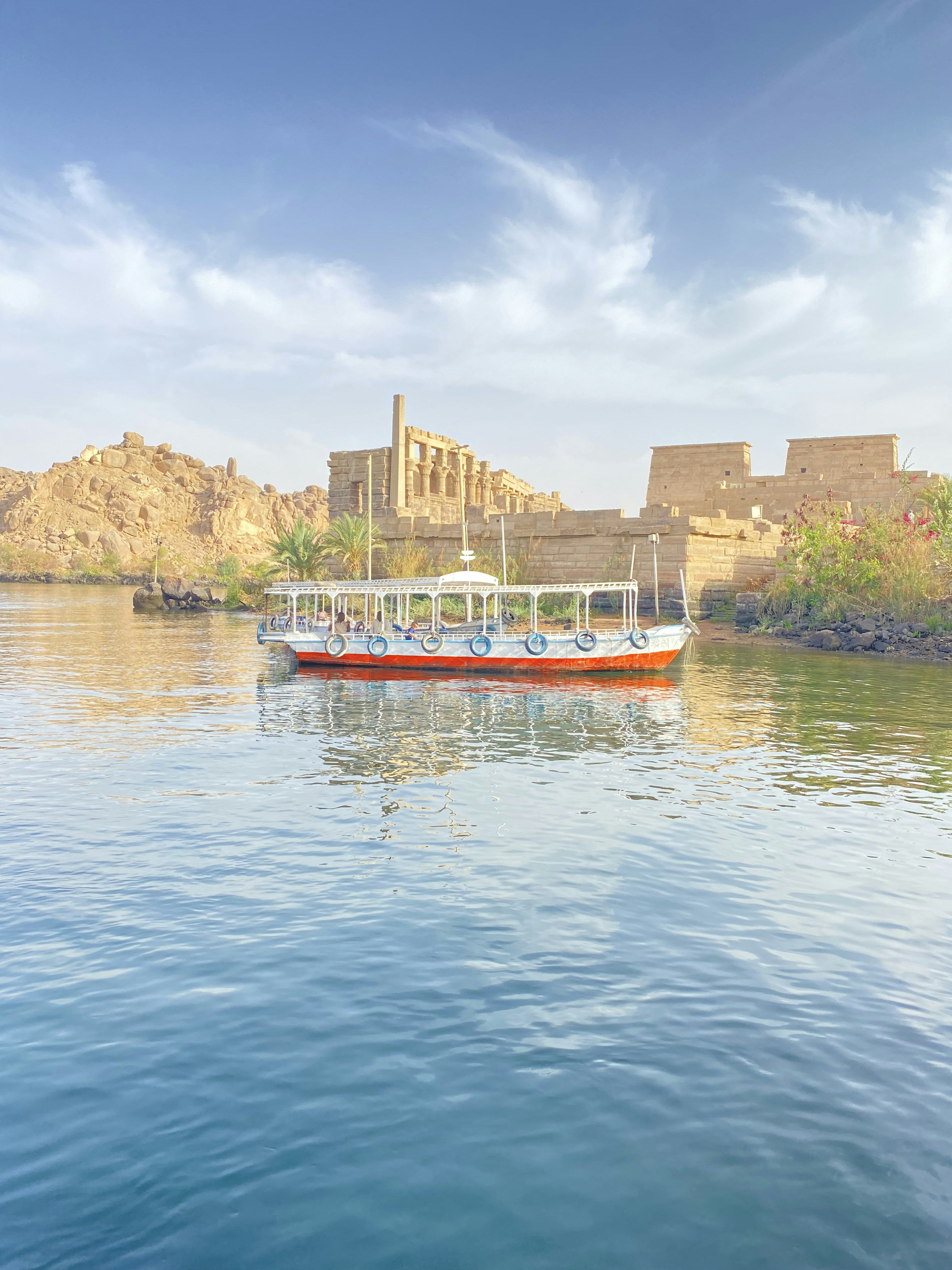 White boat navigating blue water past ancient temple ruins.