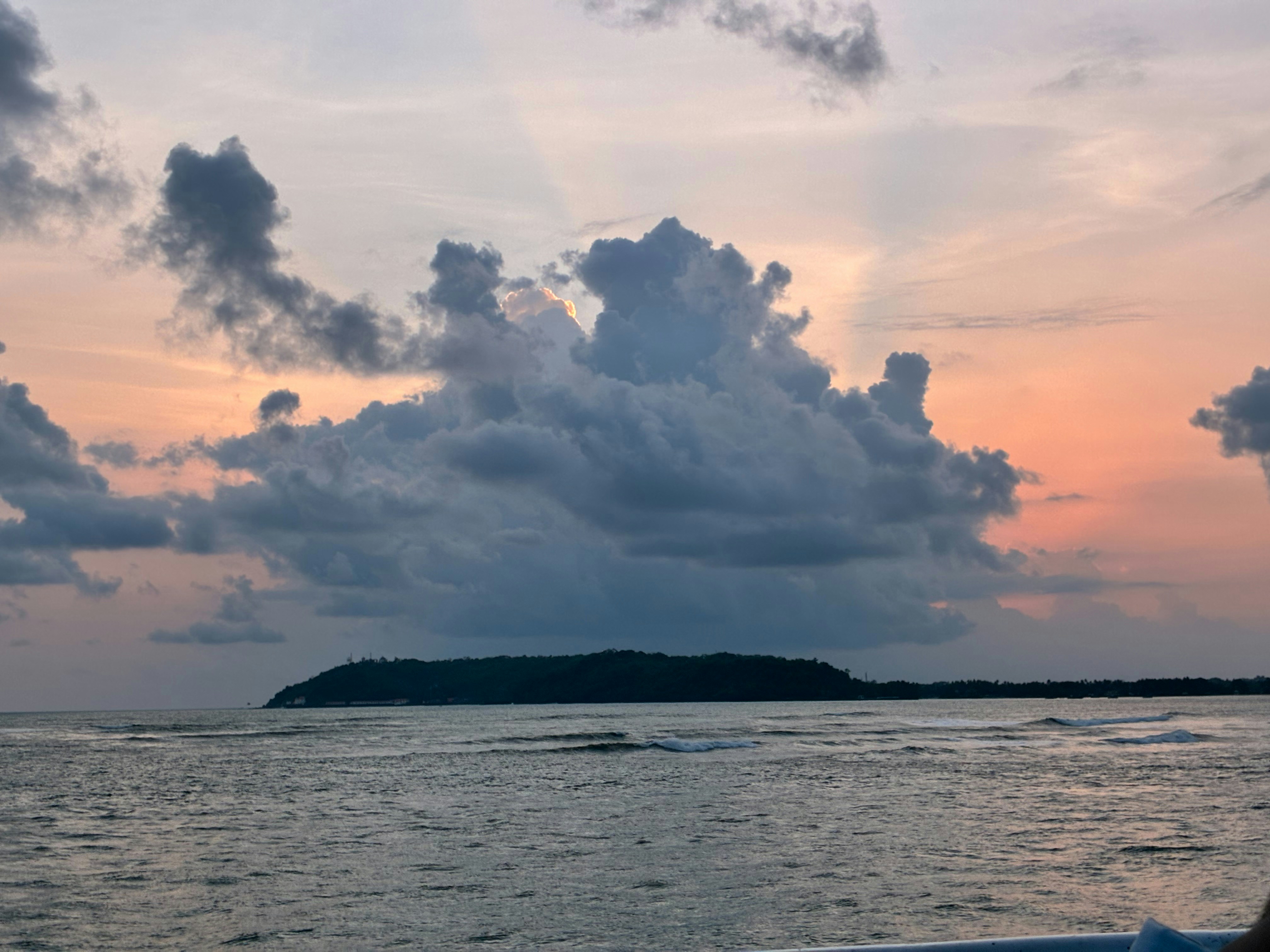 Dawn over Quiet Sea: An Island Silhouette Beneath Lifting Clouds